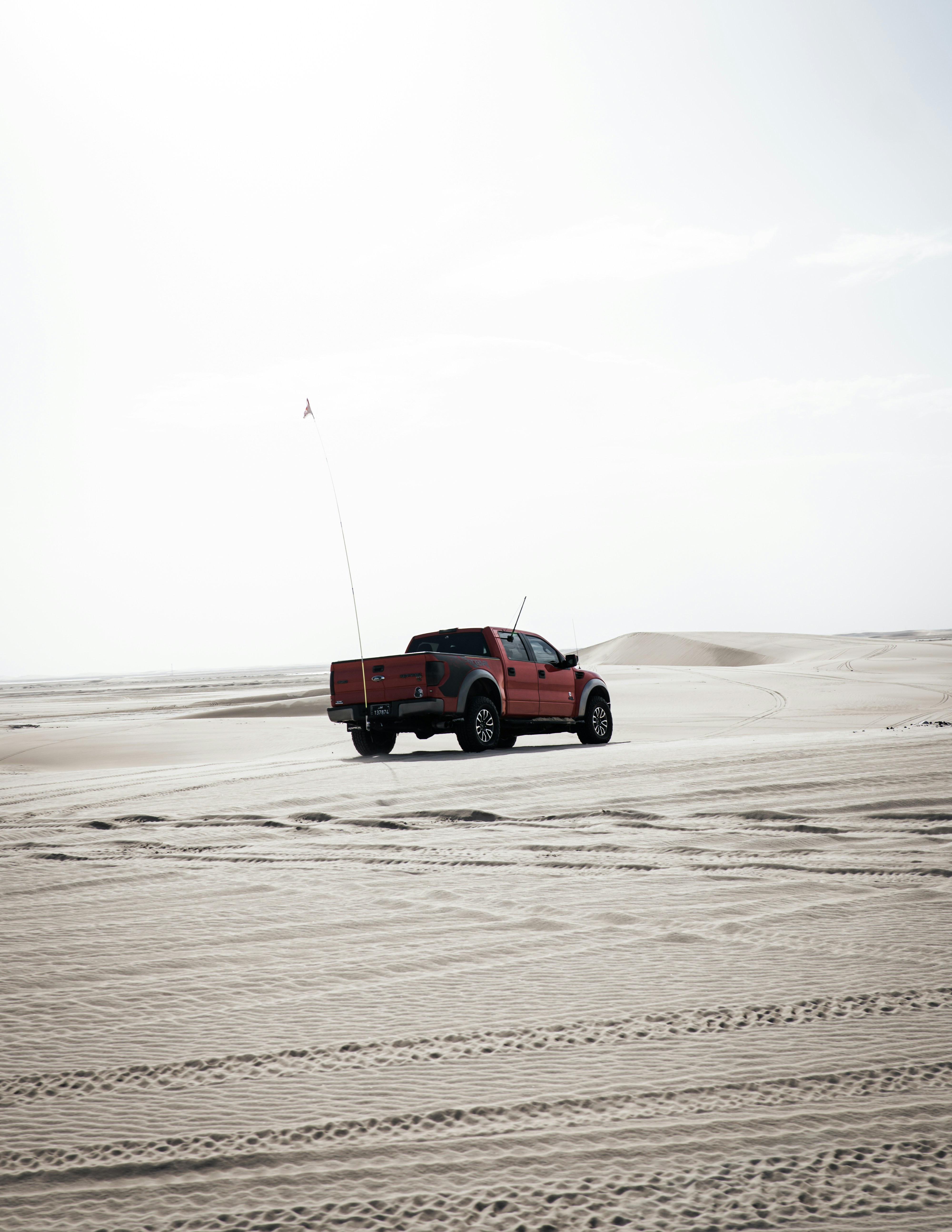 Red Pickup Roams the Dunes: A Lone Drive Across Quiet Sands