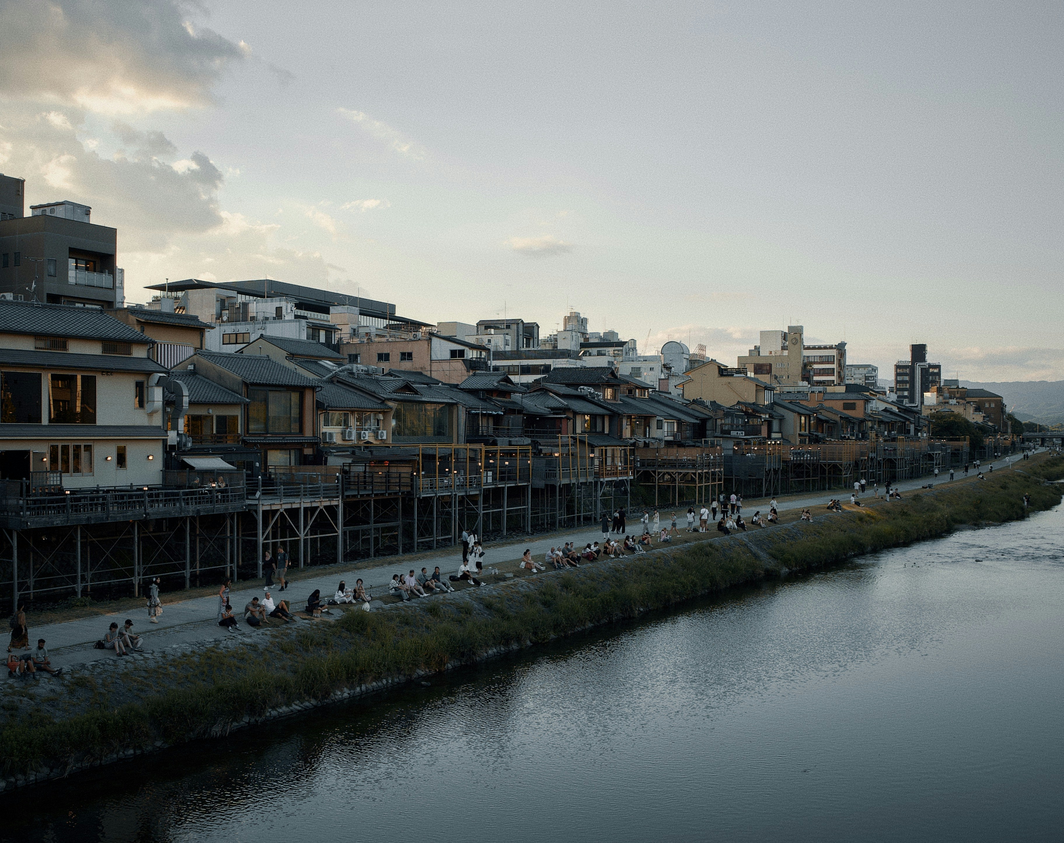 Row of riverside houses lining a calm embankment at dusk