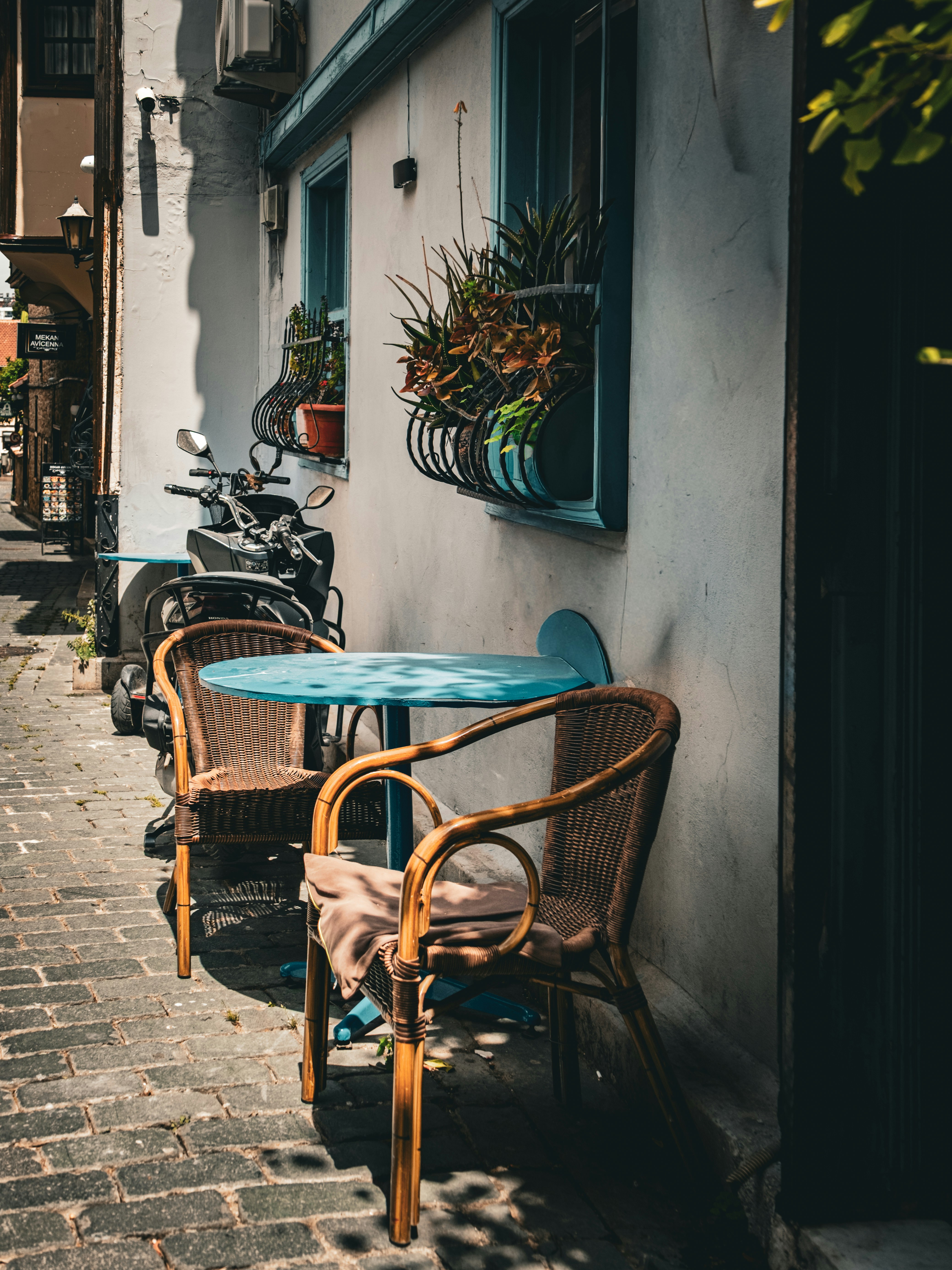 Blue-table Café Corners: Sunlit Chairs by a Quiet Cobblestone Alley