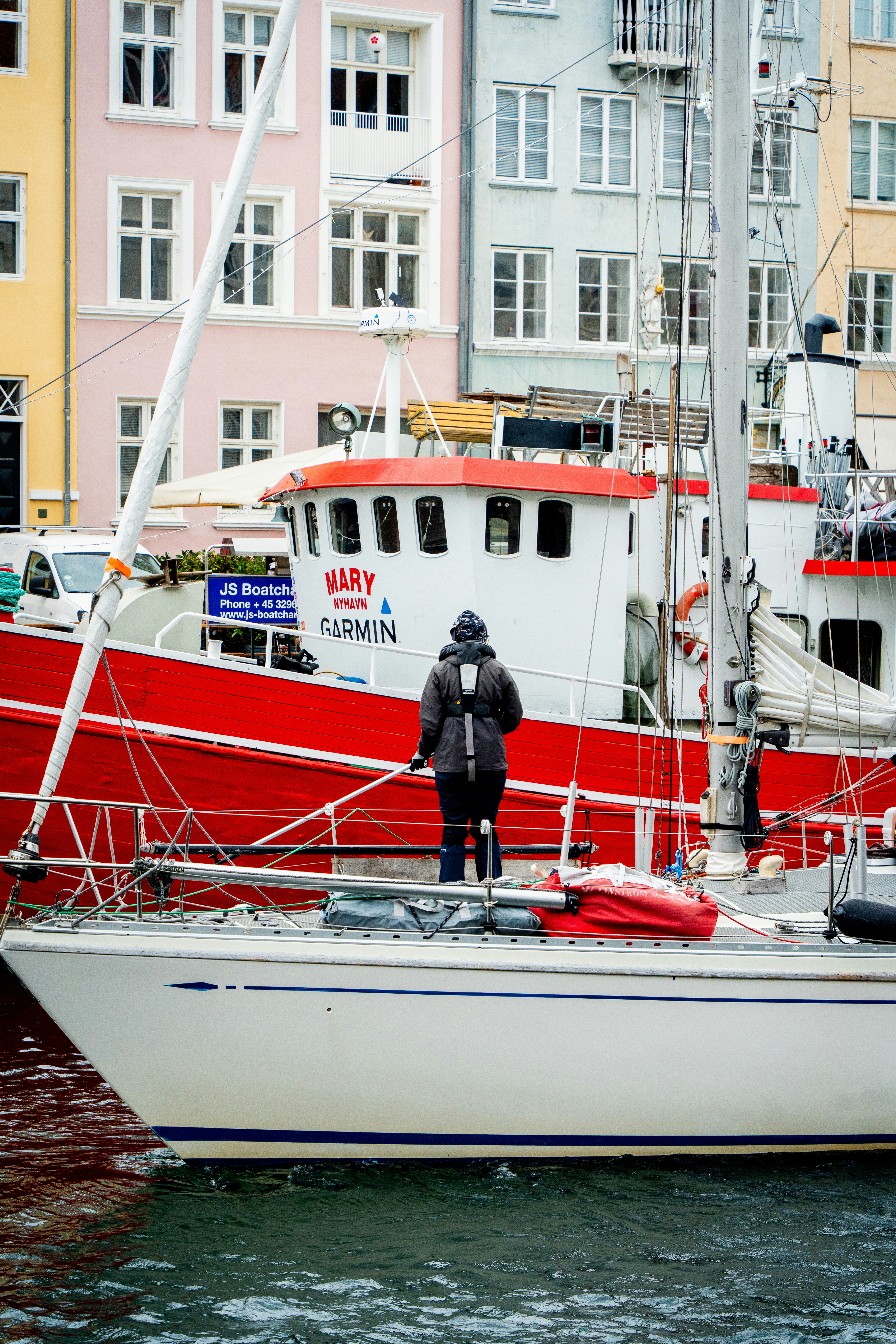 Harbor Portrait: A Sailor Stands Beside a Red Vessel among Colorful Townhouses