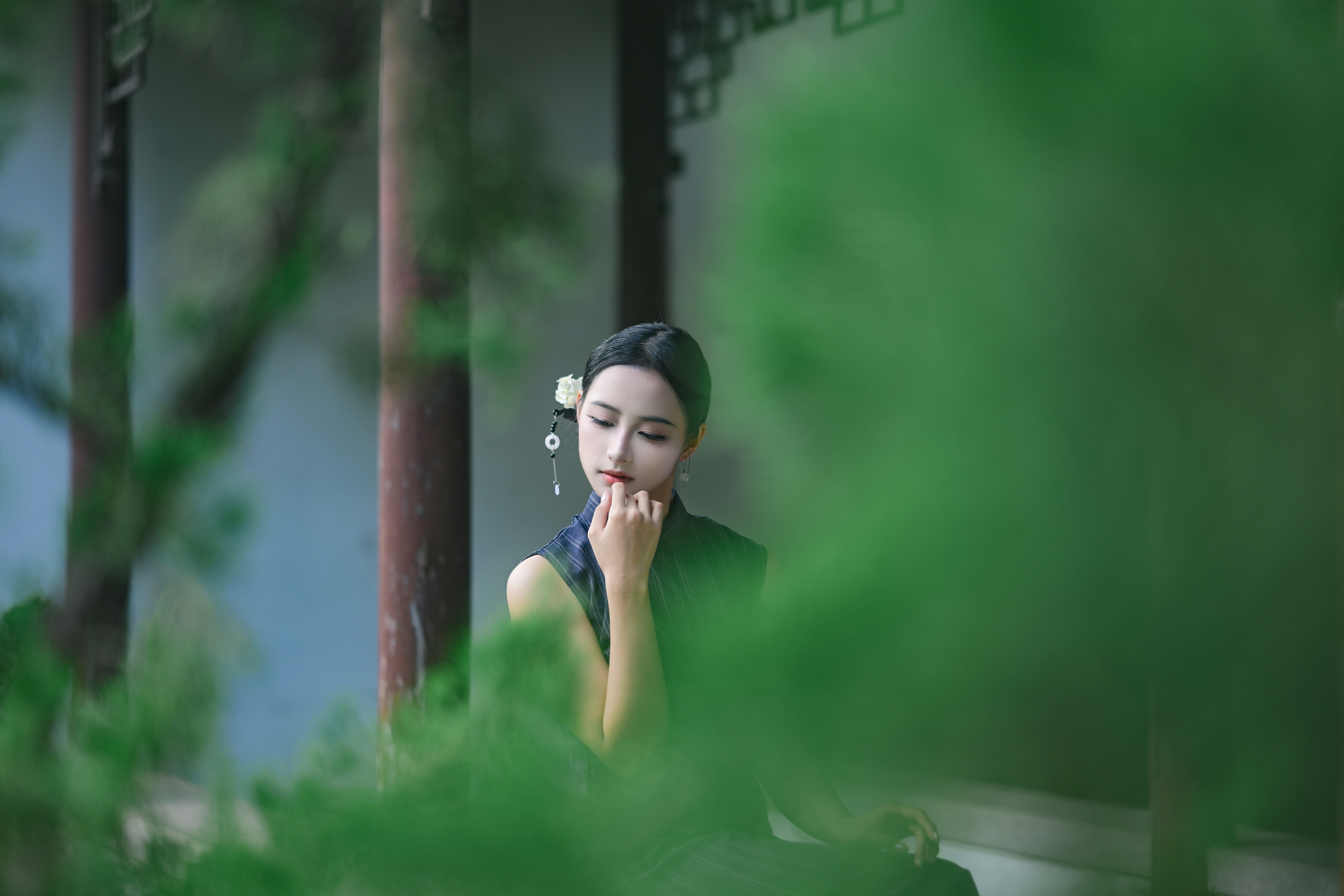 A woman in a dark cheongsam with a floral hair accessory in a garden