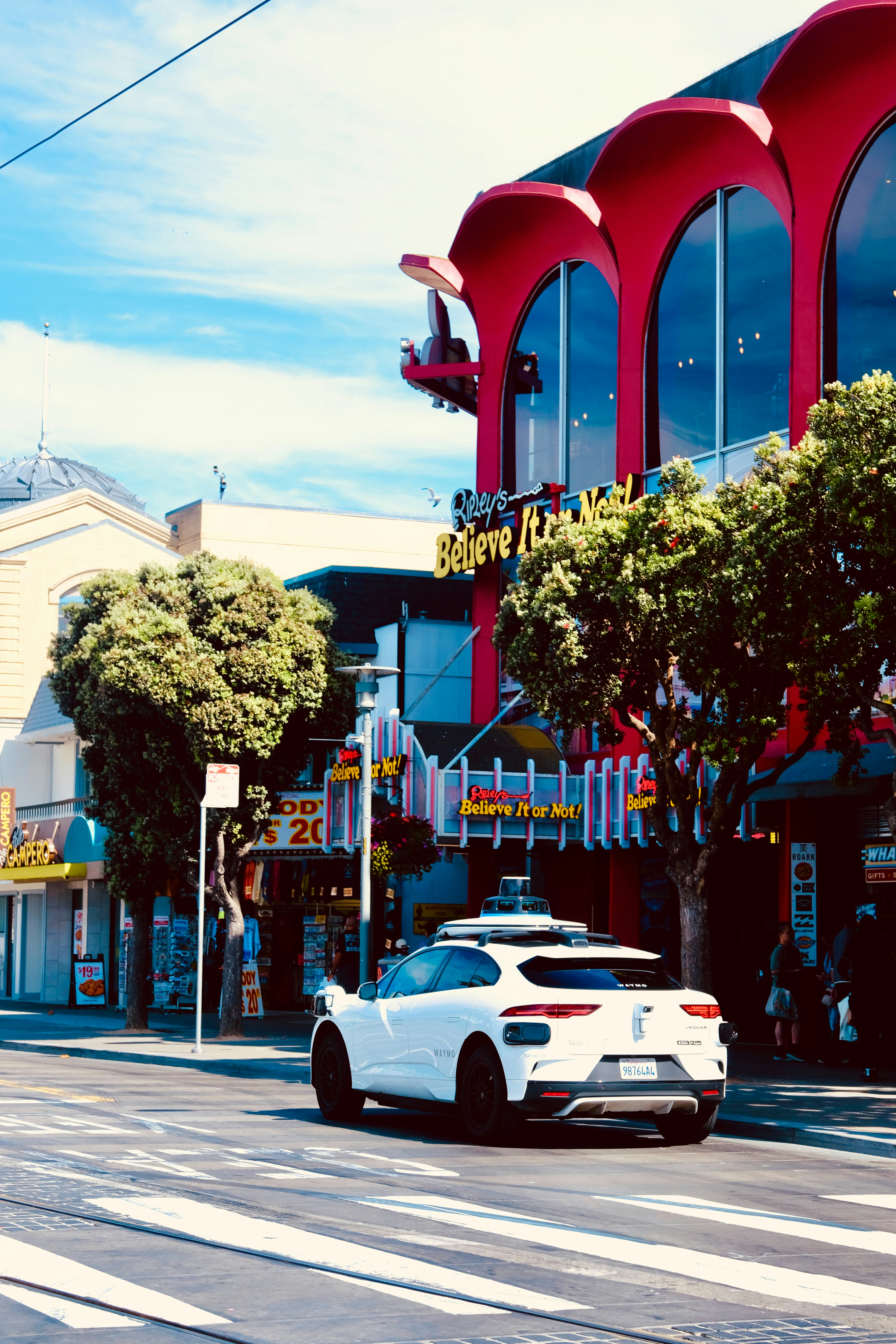 White SUV Under the Red-Arched Facade on a Busy Coastal Street