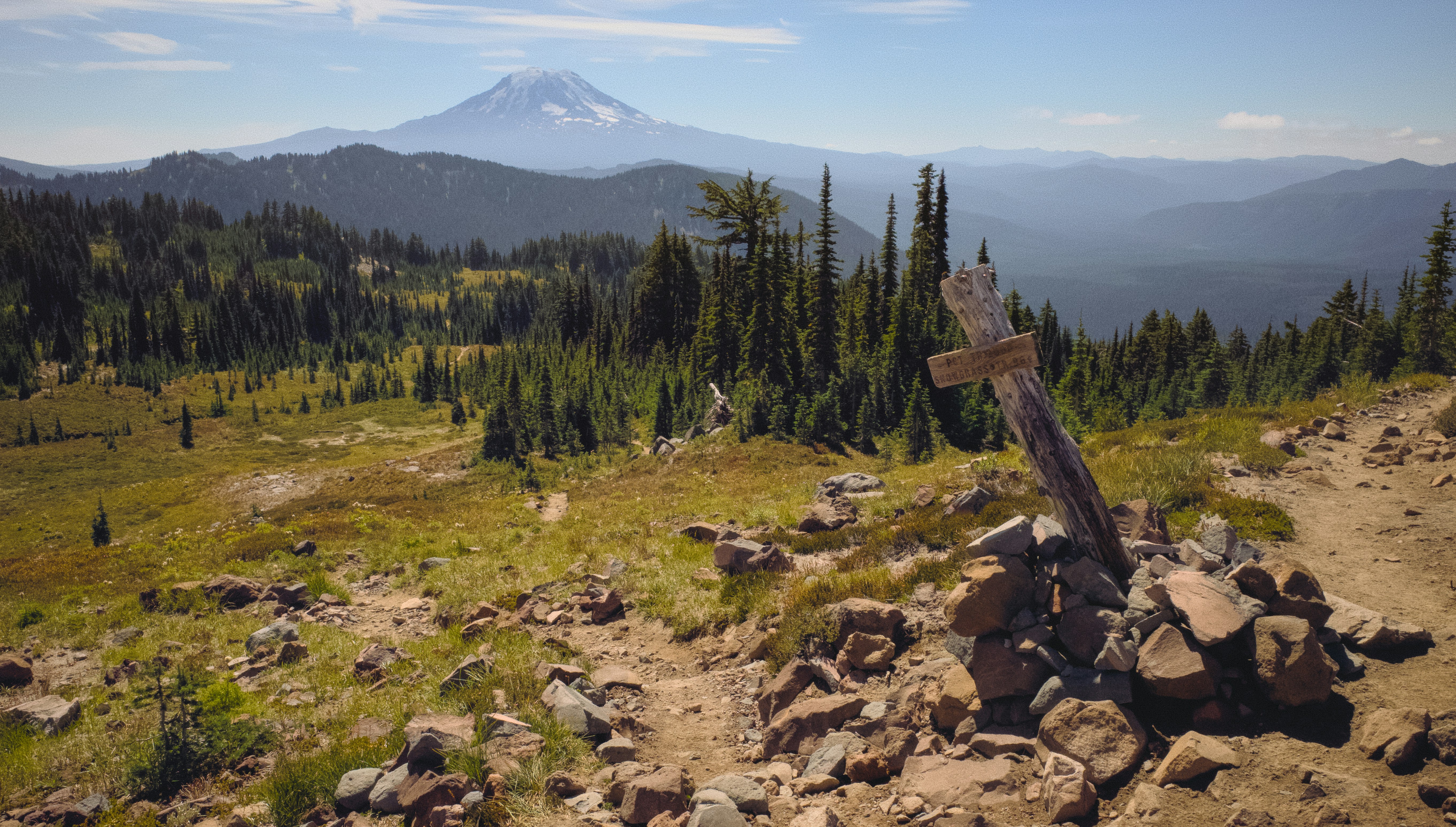 Mt. Hood silhouette over alpine meadow with cairn and log cross