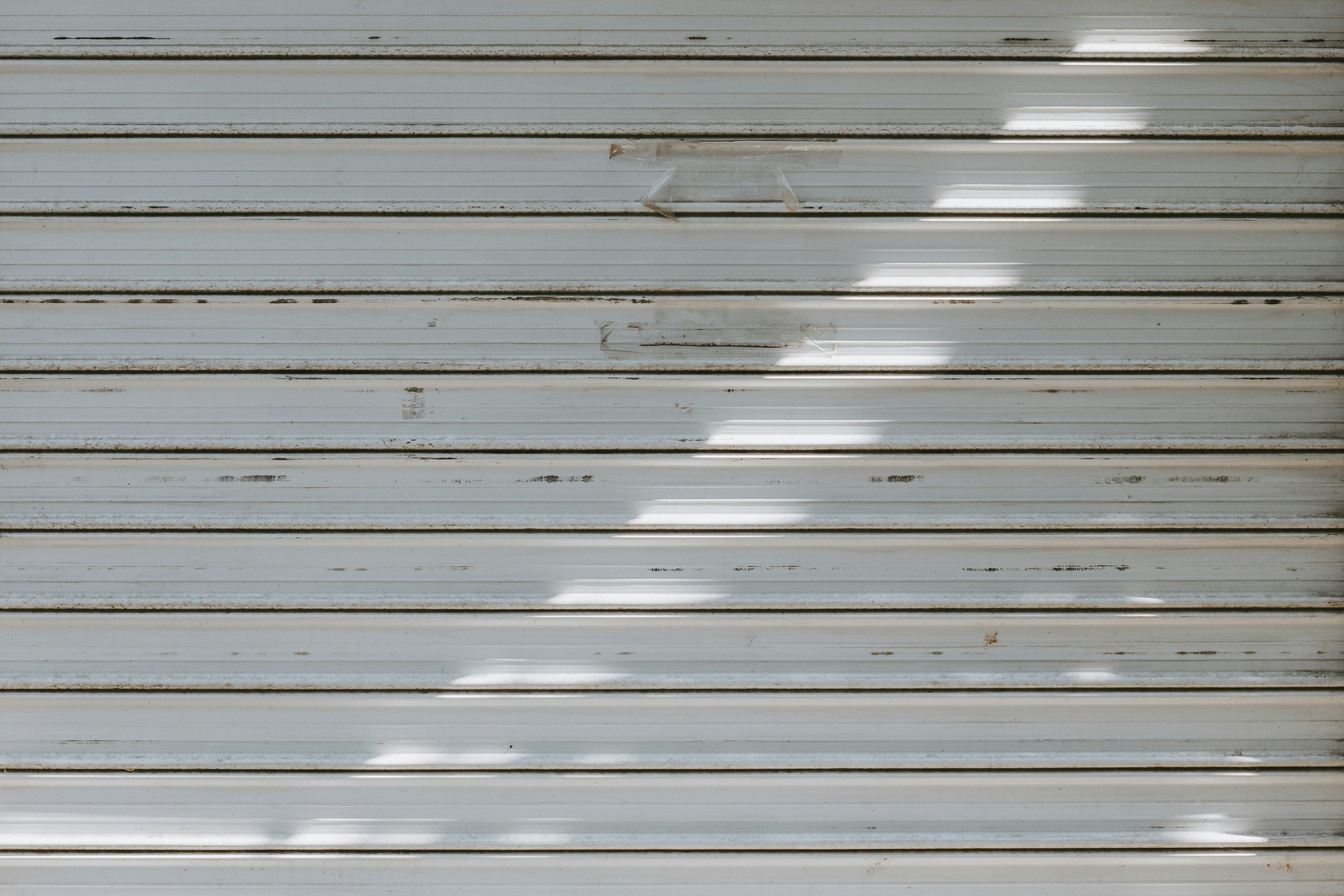 Weathered metal slats run horizontally with diagonal patches of light creating a soft, geometric pattern.