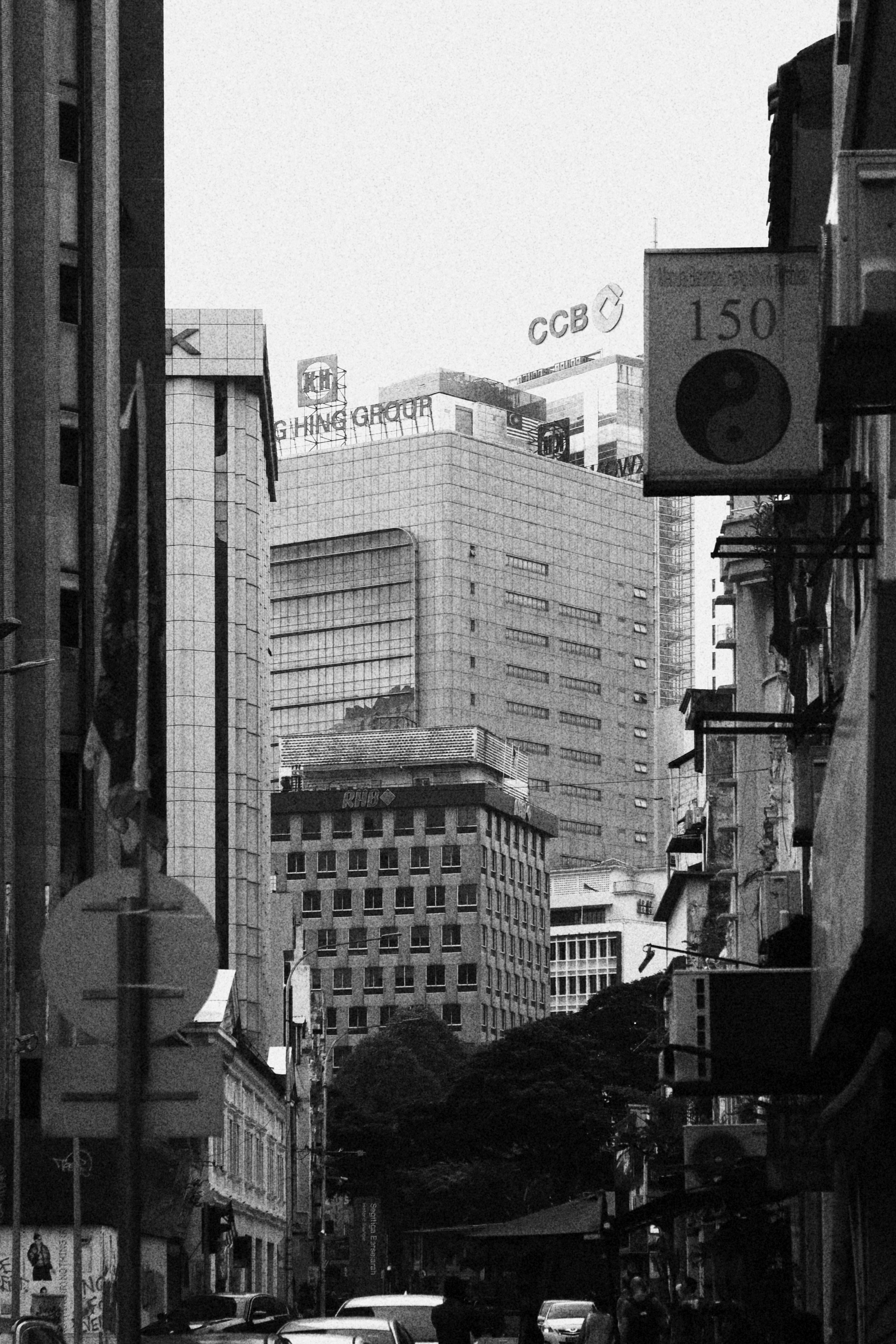 Monochrome city street with towering office buildings, a narrow pedestrian corridor, and signage; a stark, urban scene captured with a classic grayscale palette.