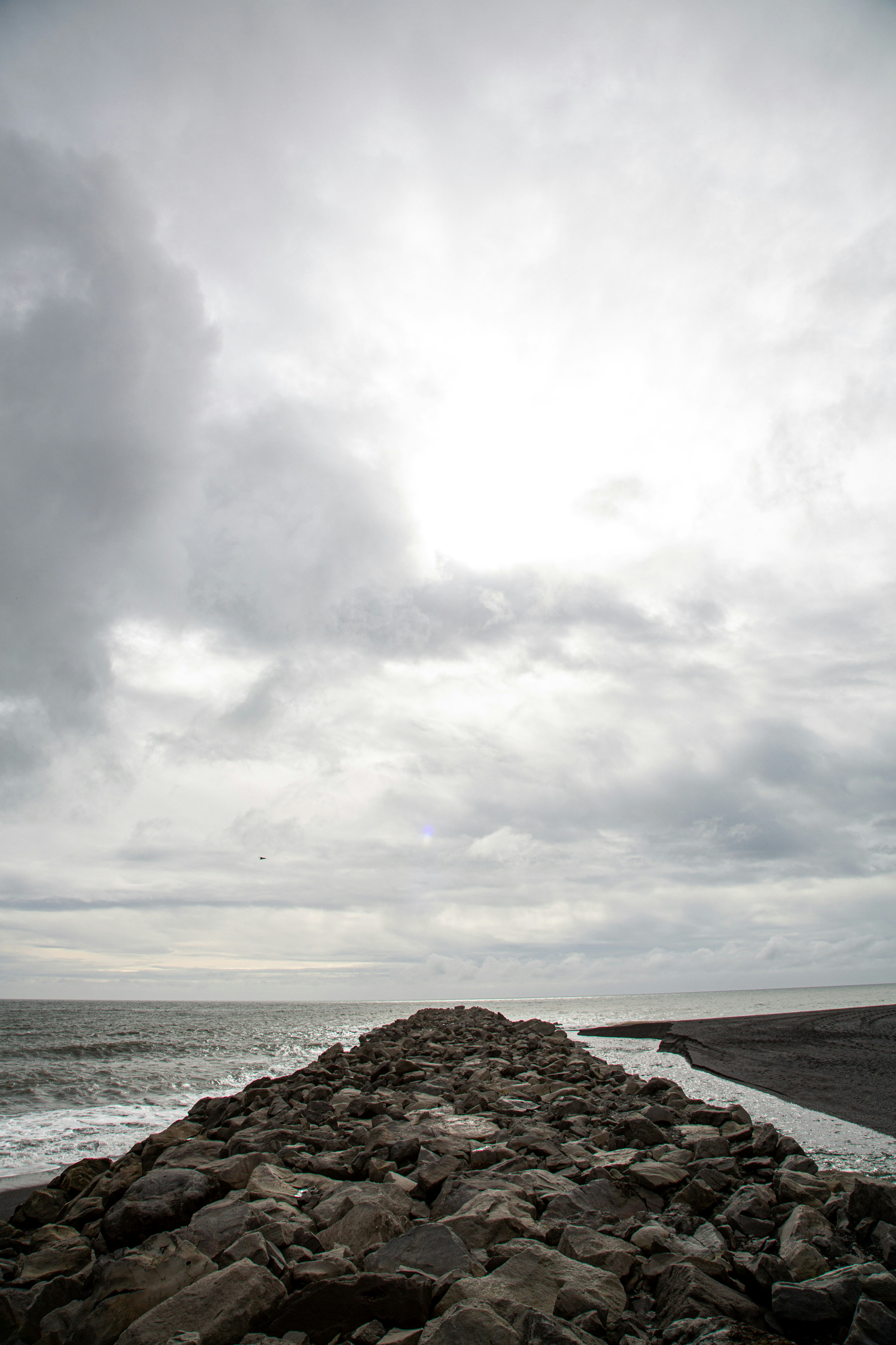 Breakwater to the Horizon: A Rocky Pier Reaches the Calm Sea Under Overcast Skies