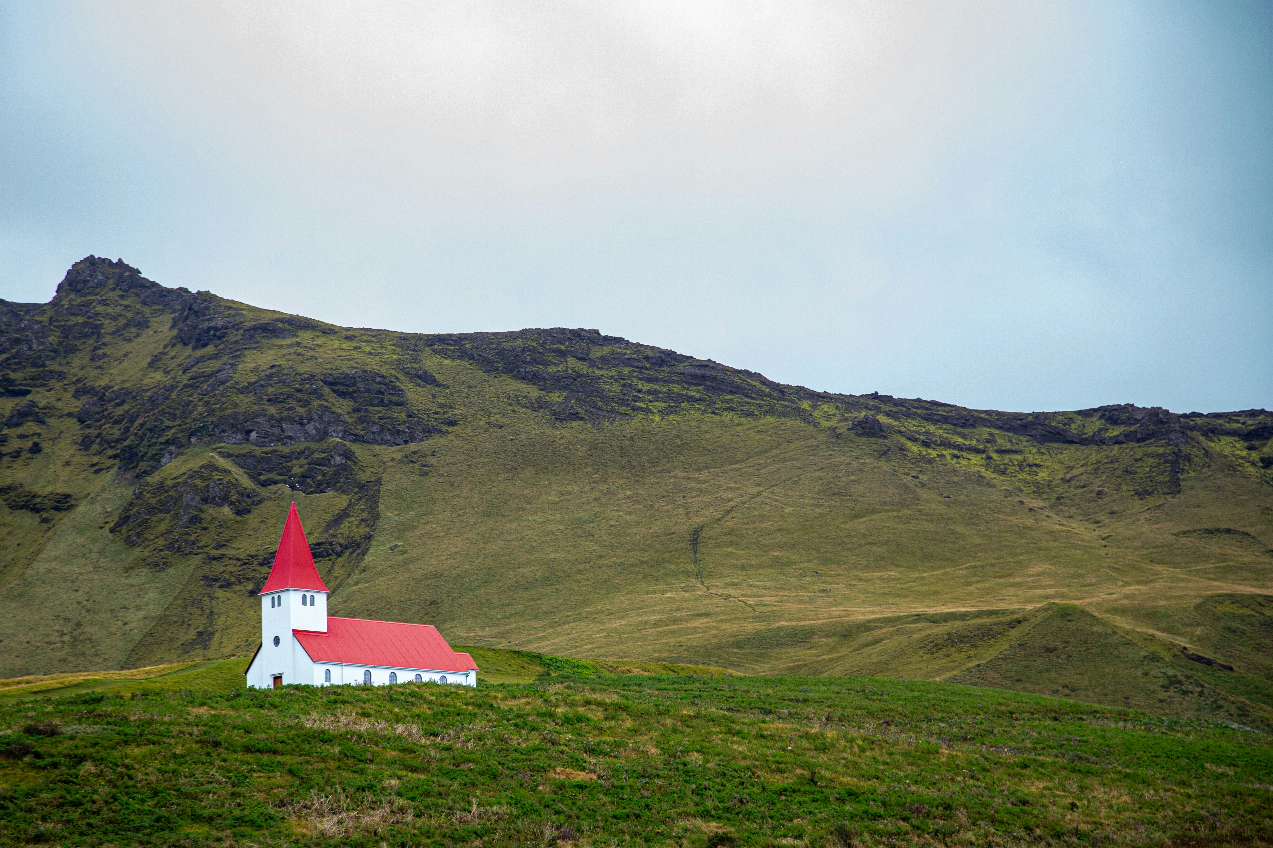 Red-roofed chapel on a rolling hillside under a soft Icelandic sky