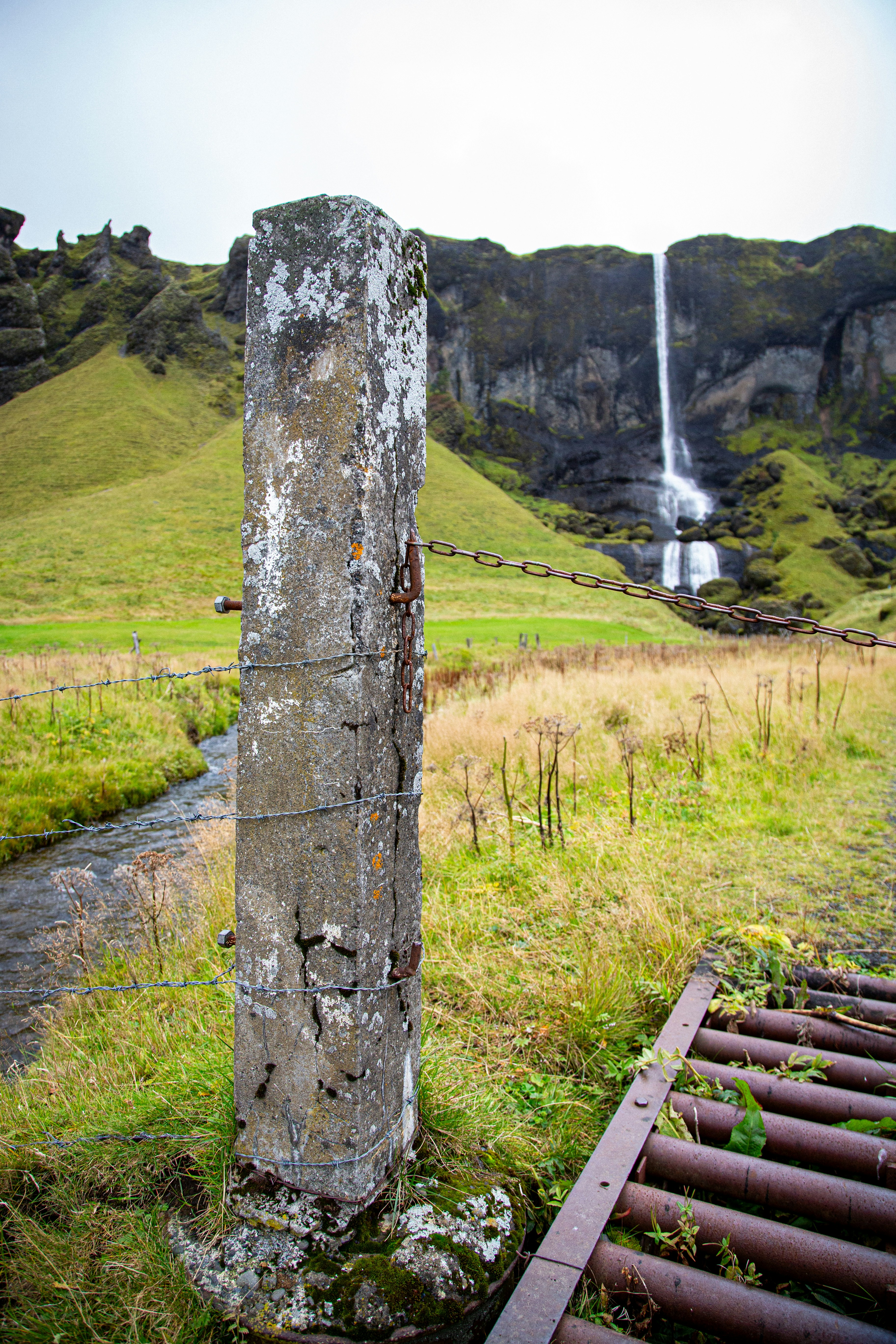 Weathered Post and Cascading Falls: A Quiet Border Between Field and Cliff