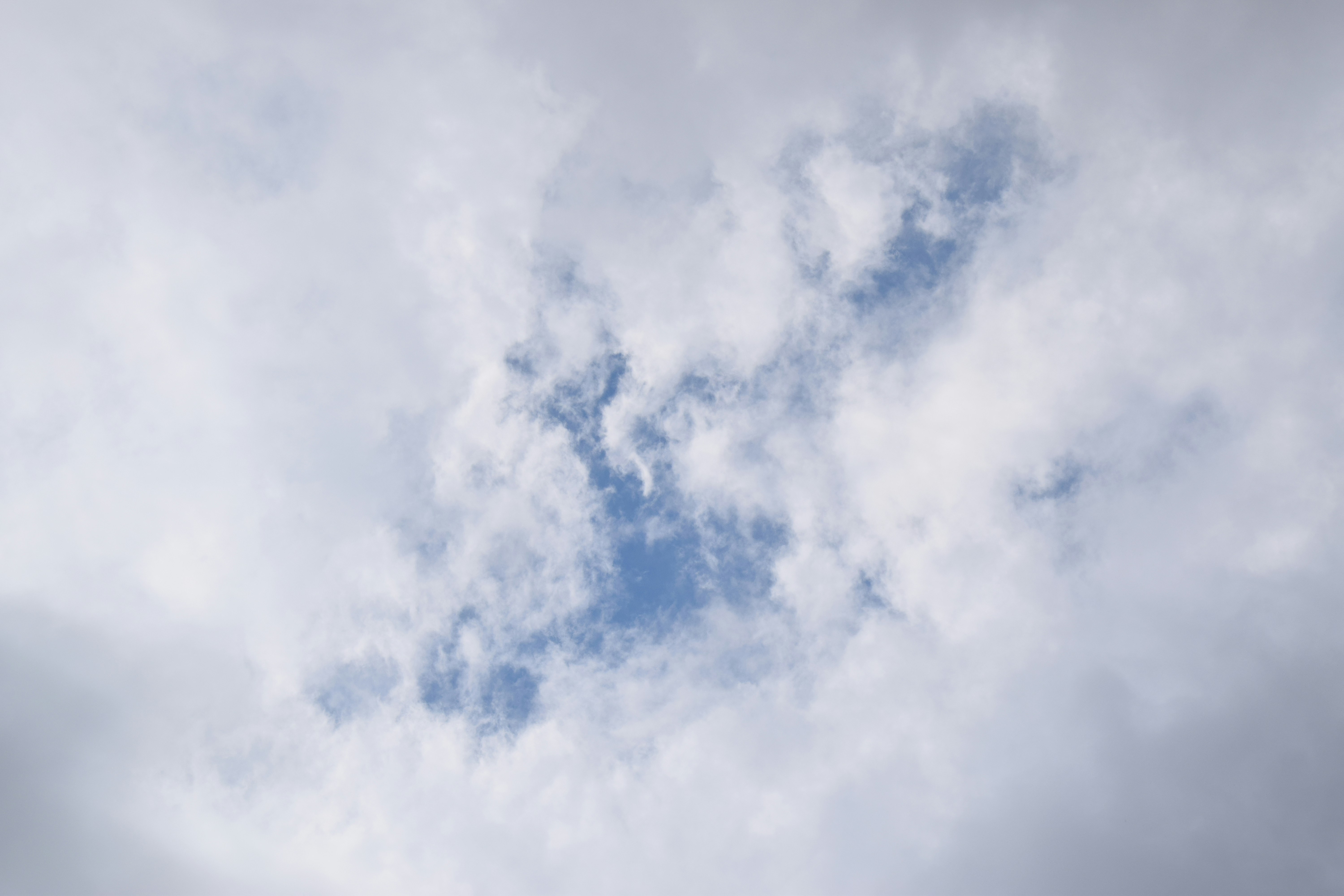 Soft clouds drift across a pale blue sky, with a small opening revealing blue in the center. This image emphasizes the airy atmosphere and natural light without identifiable subjects; a minimal sky shot suitable for background use.