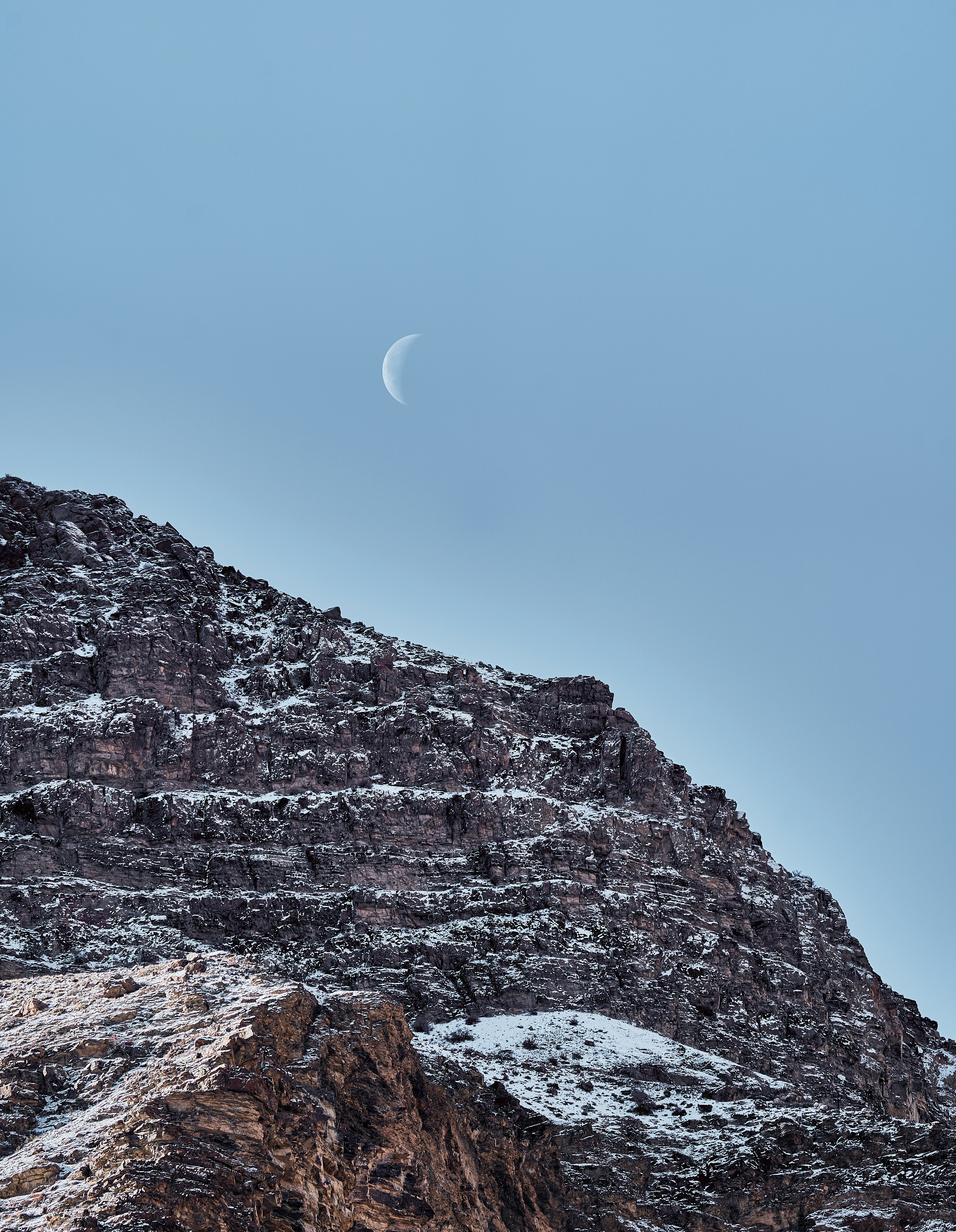 Crescent Over Crags: Snow-Capped Ridge Beneath a Pale Moon