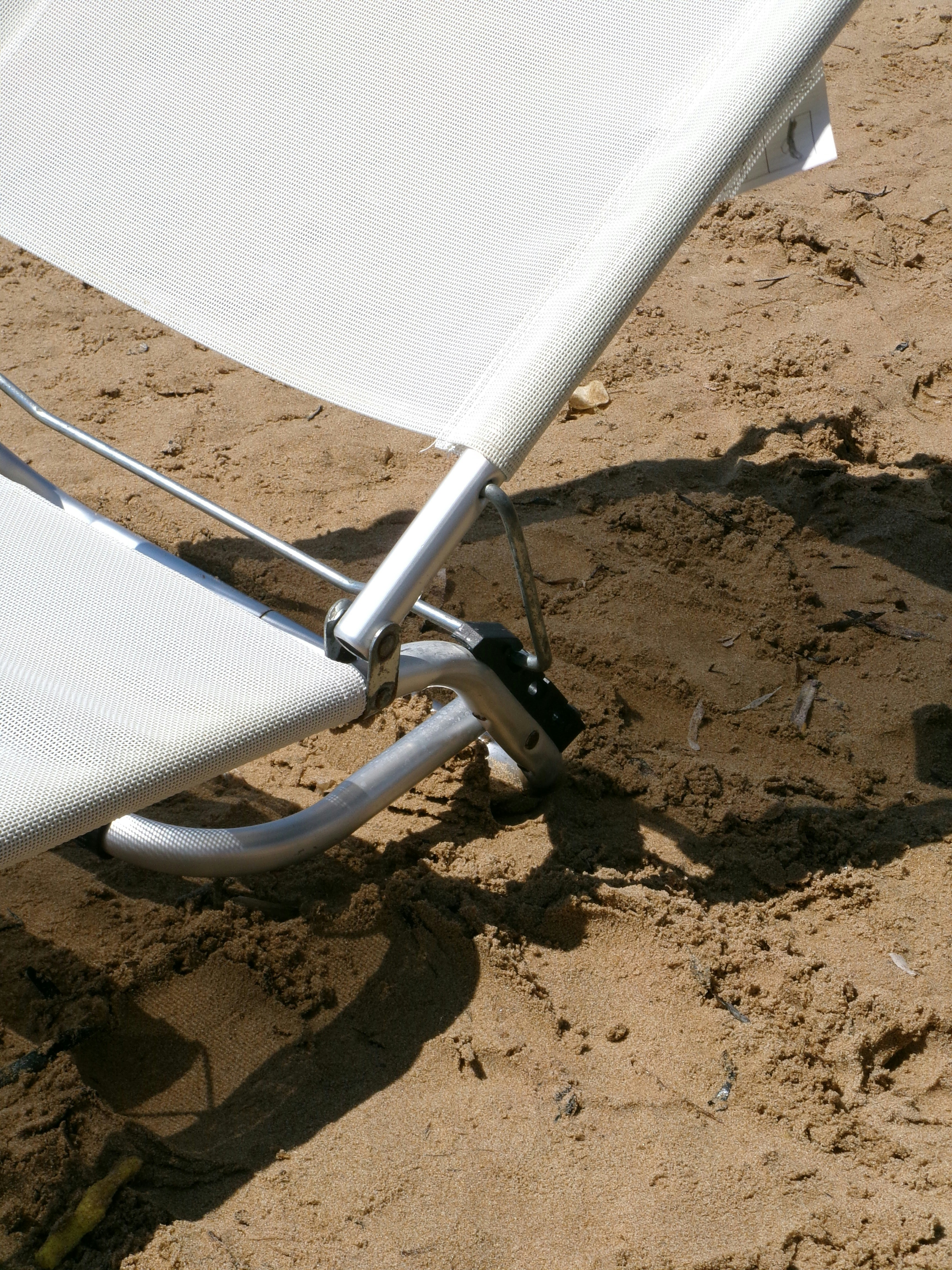 A white beach chair rests on sun-warmed sand, captured up close to emphasize the fabric texture and metallic frame against a warm beach backdrop.