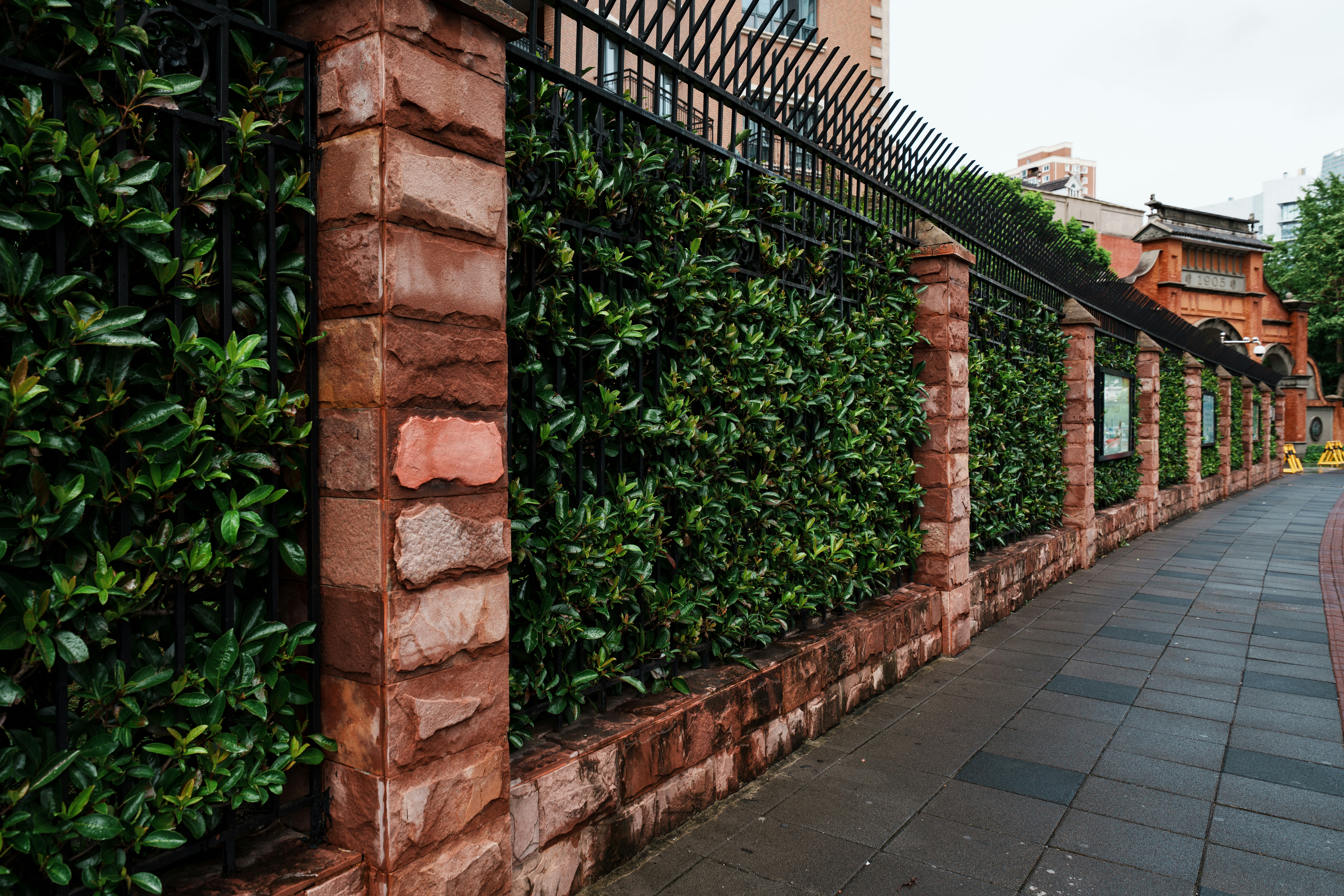 Brick-and-hedge corridor along a sunlit urban sidewalk