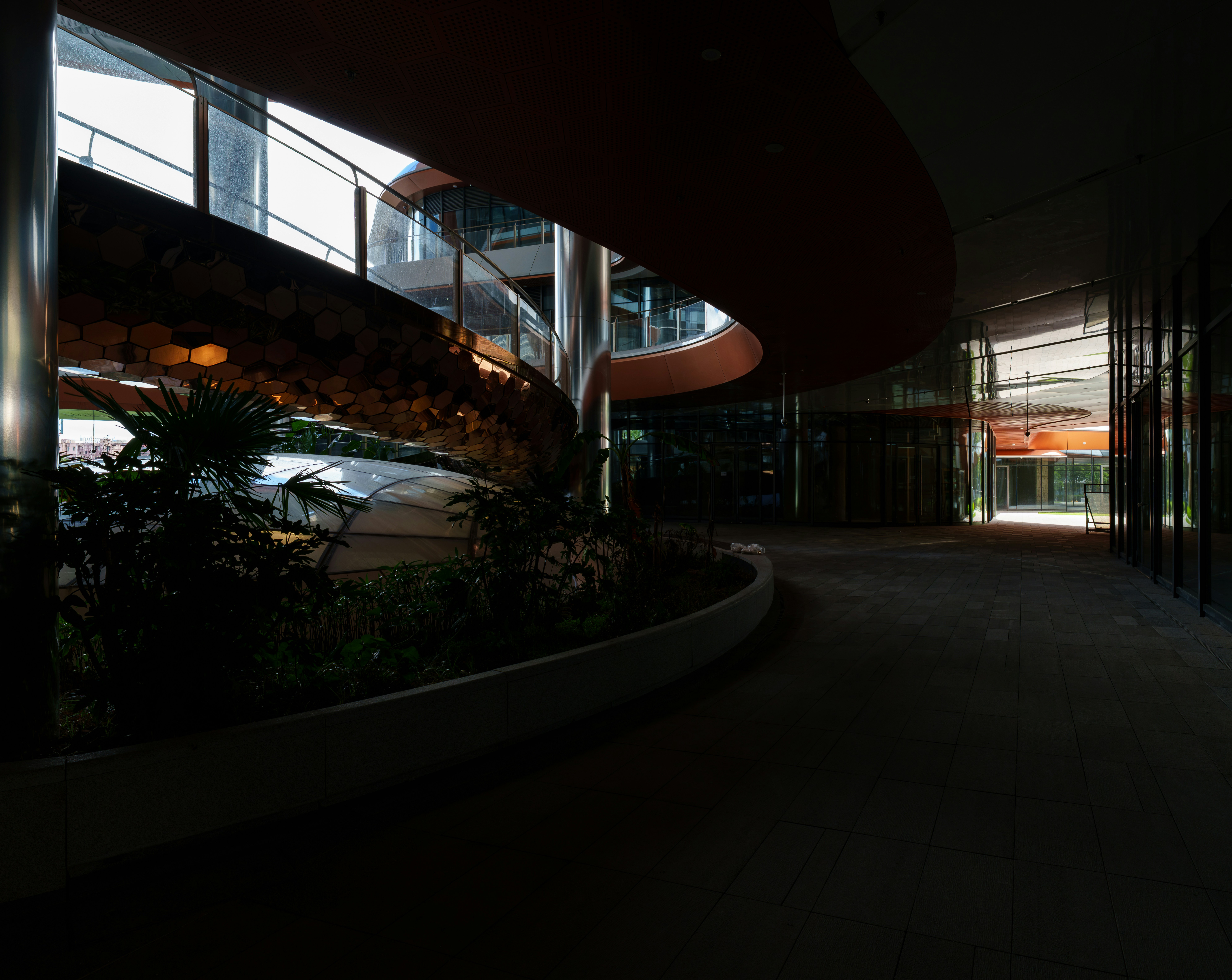Curved modern atrium at dusk: illuminated walkway and spiraling balcony