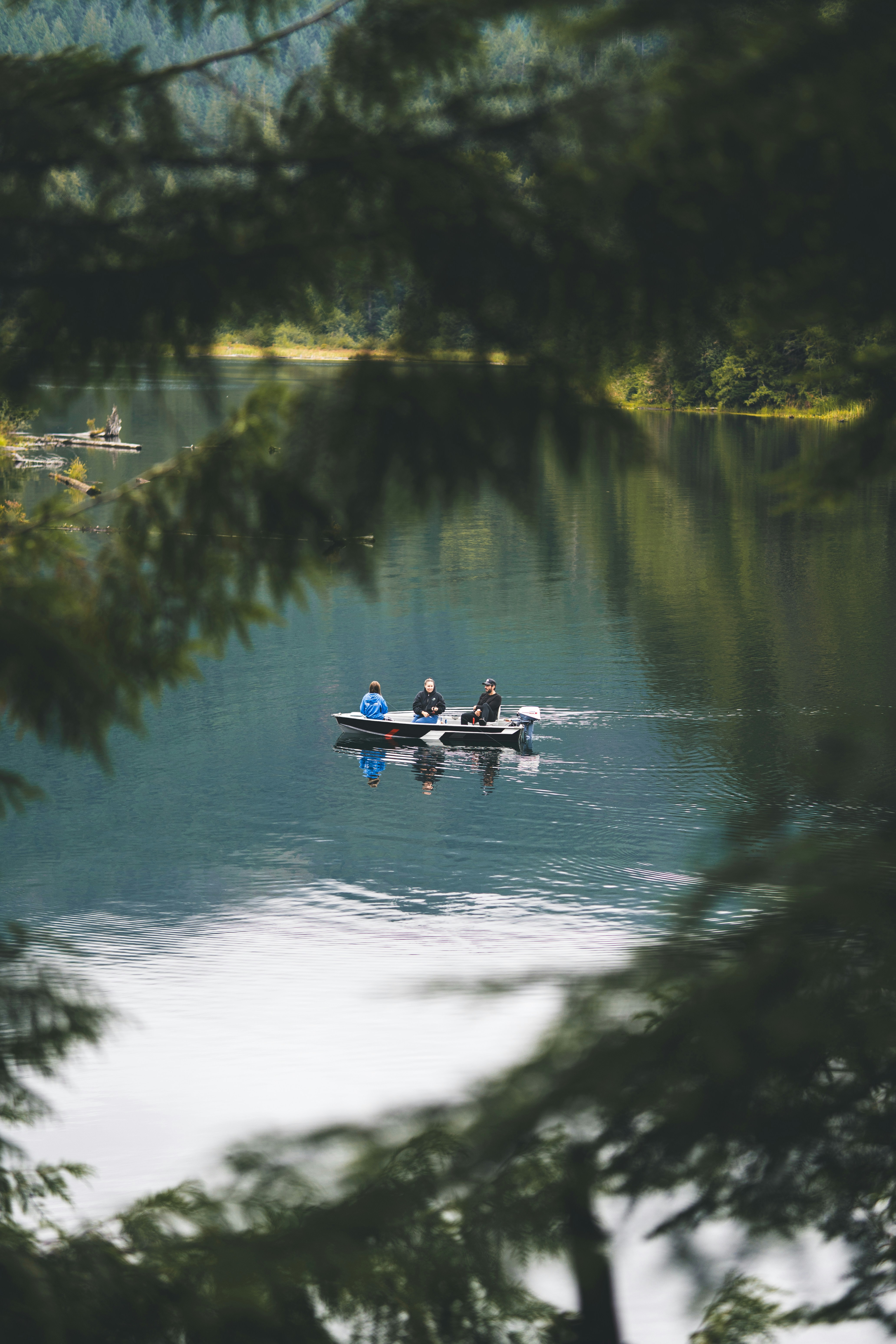 Three Anglers Drifting Across a Glassy Lake Framed by Fern-Laced Branches