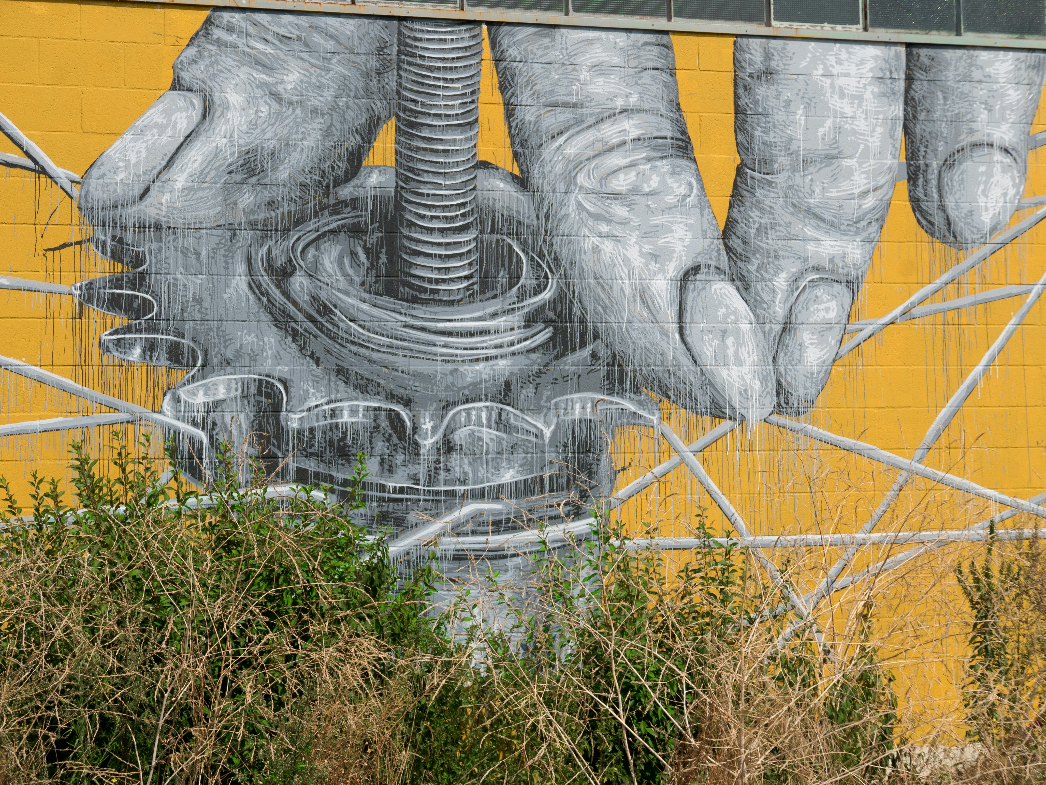 Gears of Community: A Giant Hand Sculpted in Concrete Adrift over a Yellow Wall