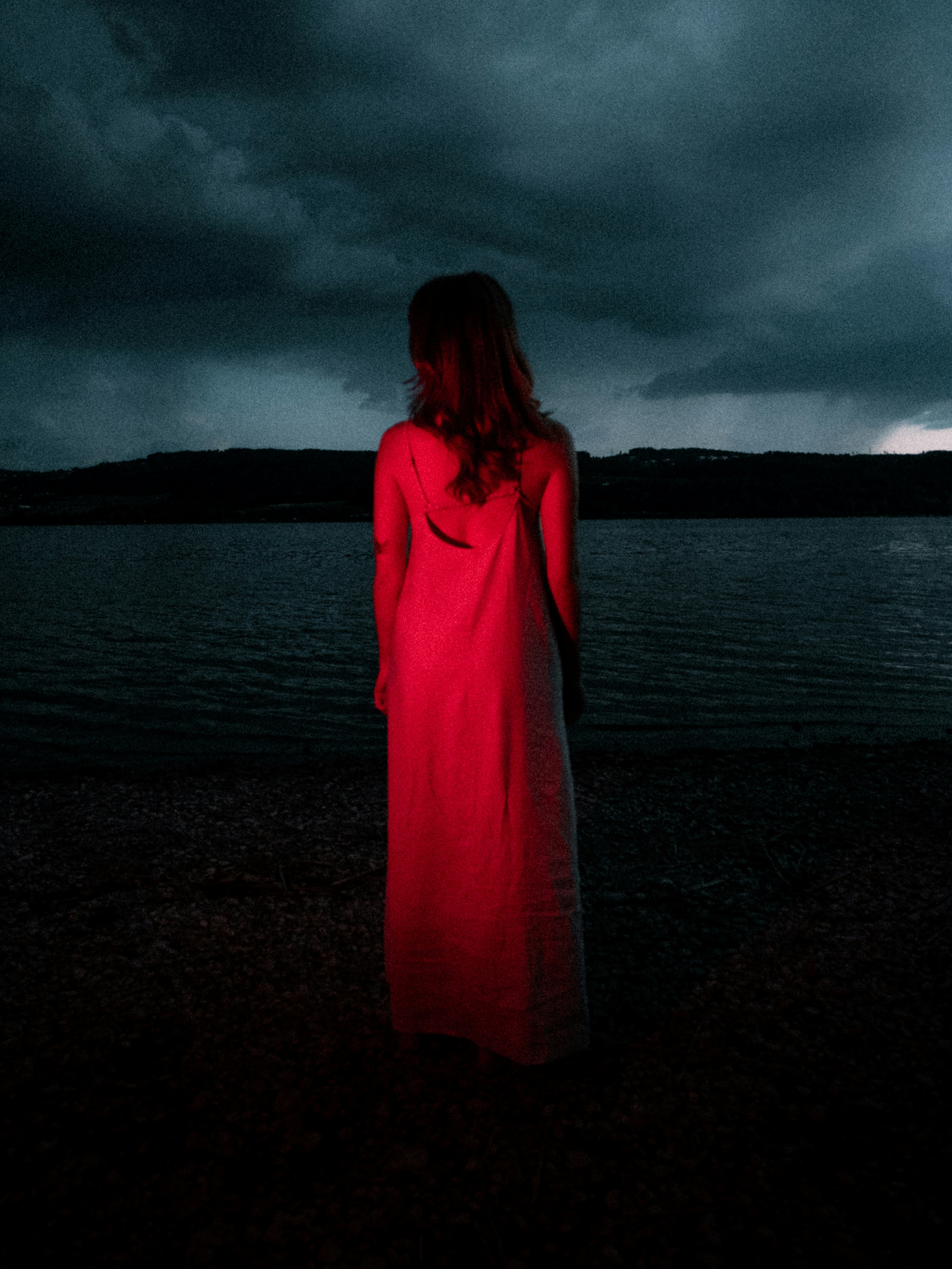 Red-Illuminated Figure at a Storm-Scarred Shore