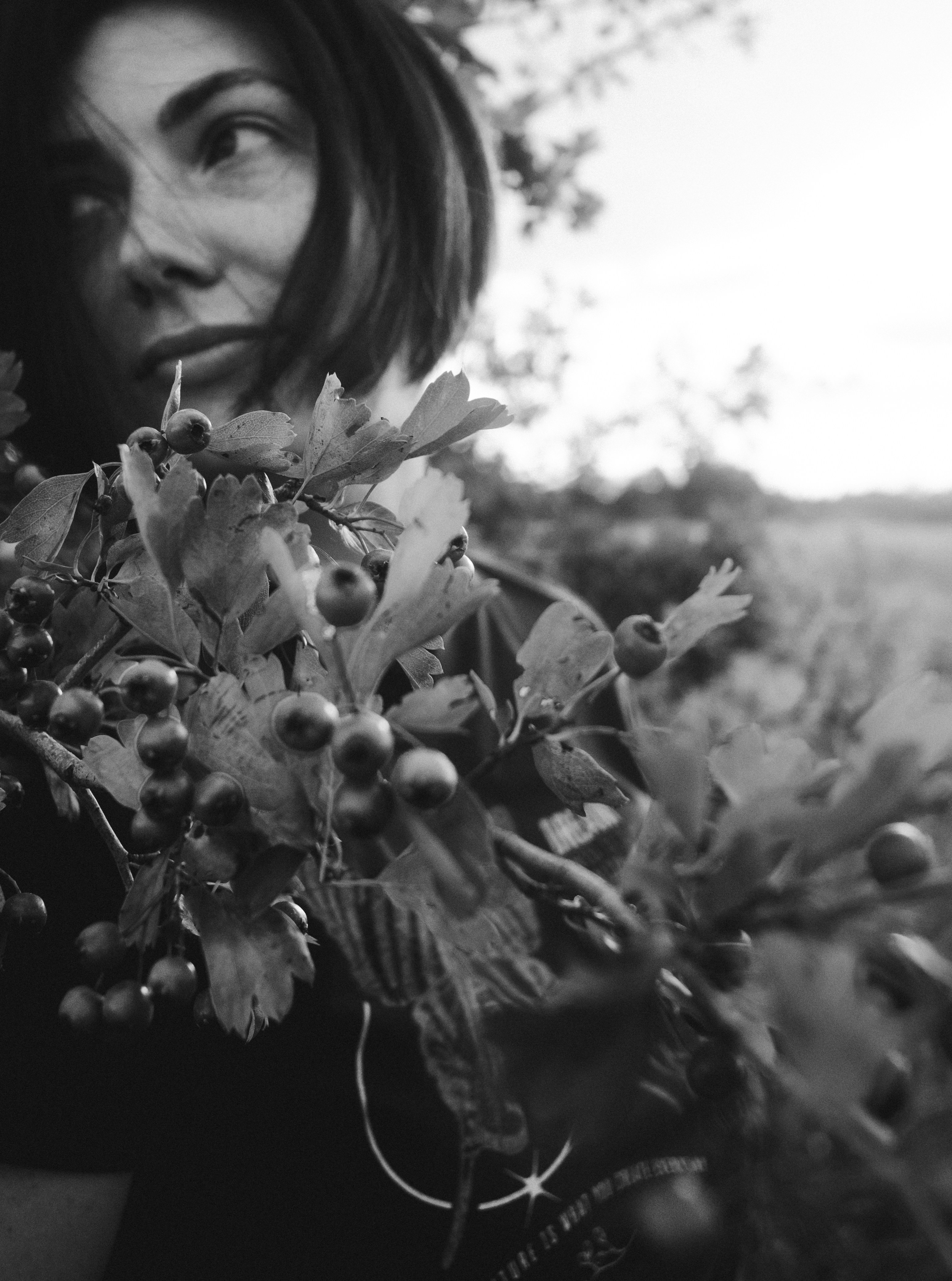 Monochrome portrait with the subject partially obscured by foreground berries and leaves, creating depth and mystery.