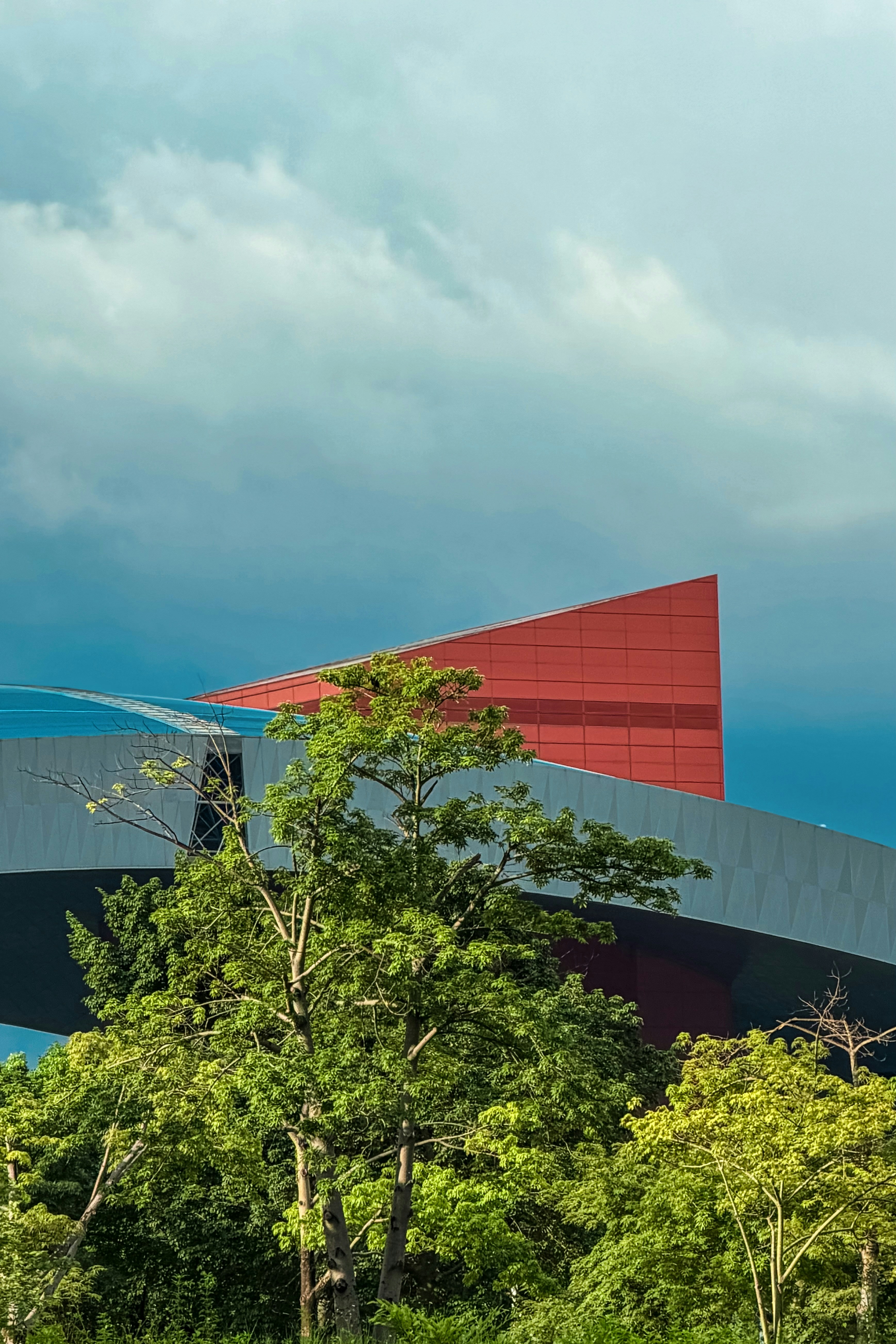Red Roof Peaks Beyond Green Canopy Against Sky