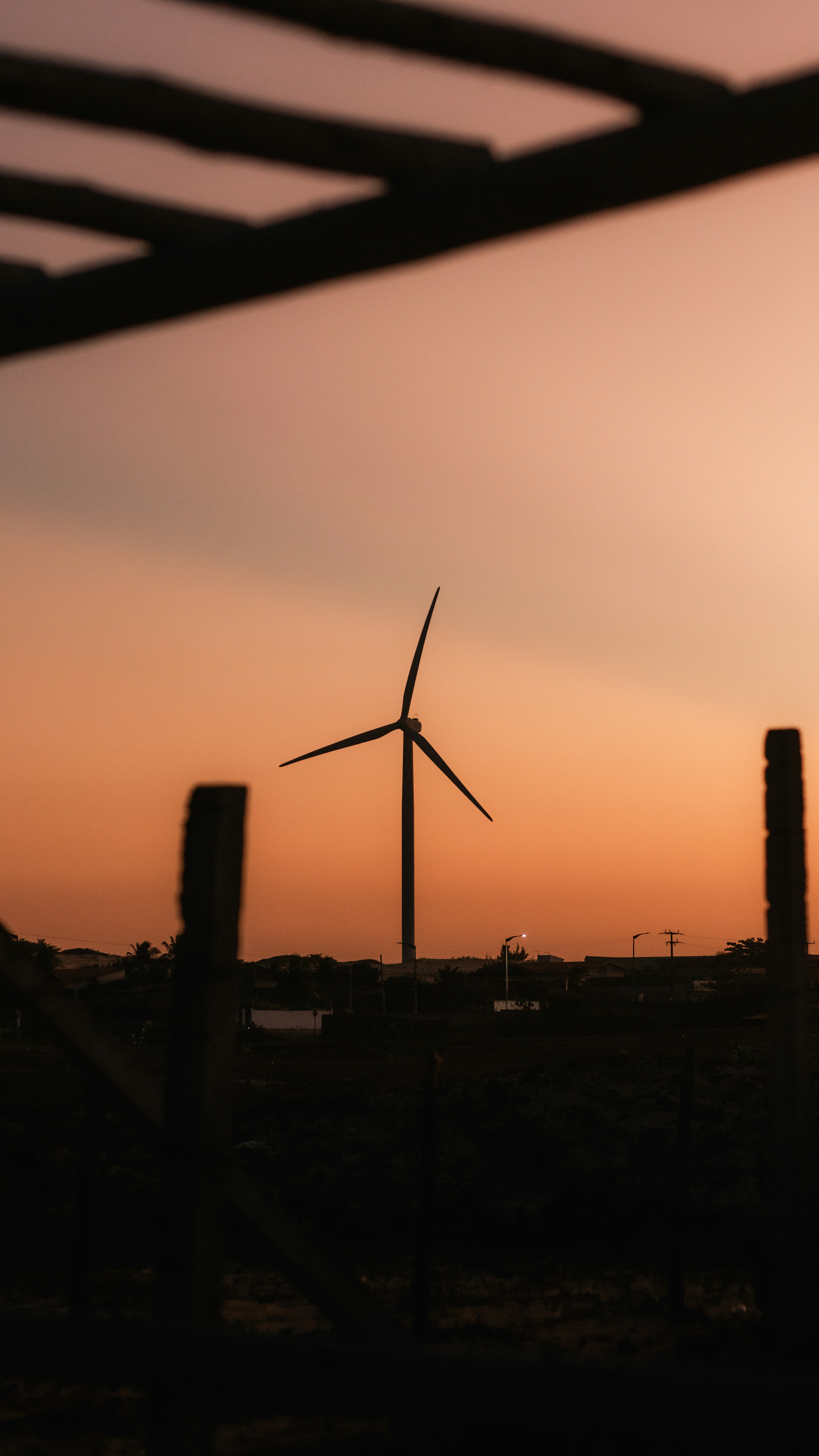 Silhouette of a Wind Turbine at Sunset Behind a Fence