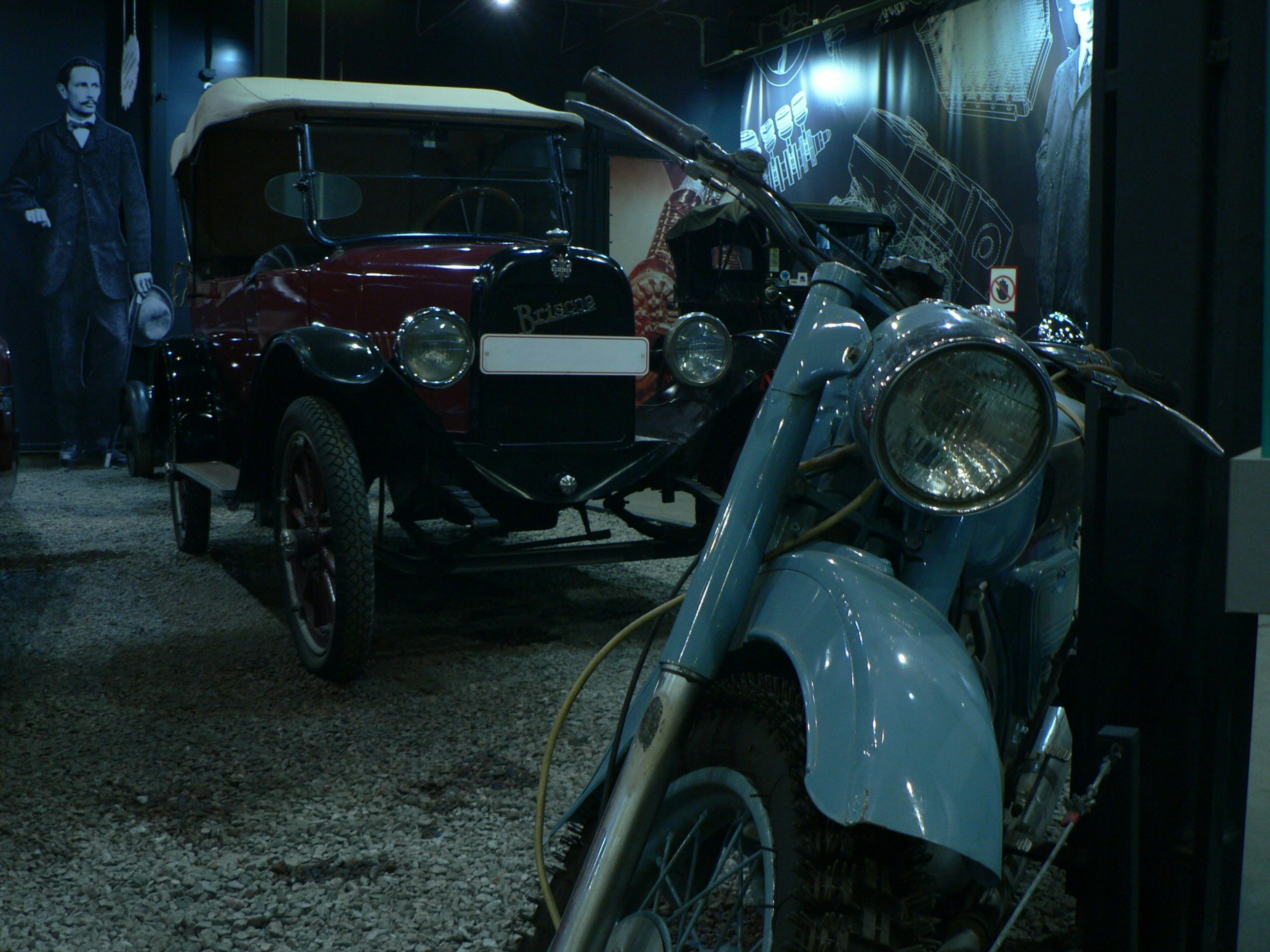 Vintage Duo: A Classic Car and a Restored Motorcycle Guard a Dim Museum Scene