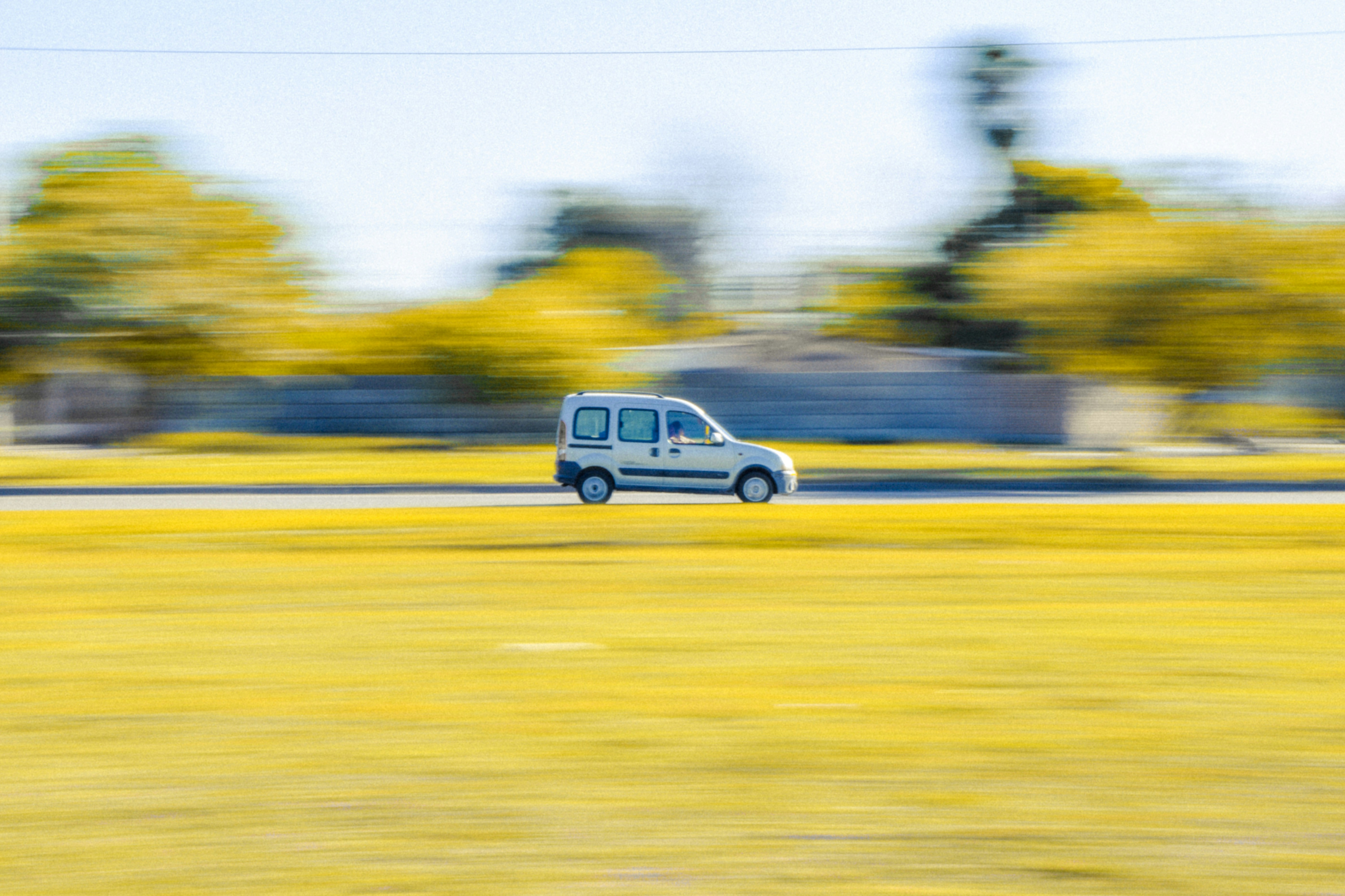 White van in a sunlit field blurs across a motion-lit landscape