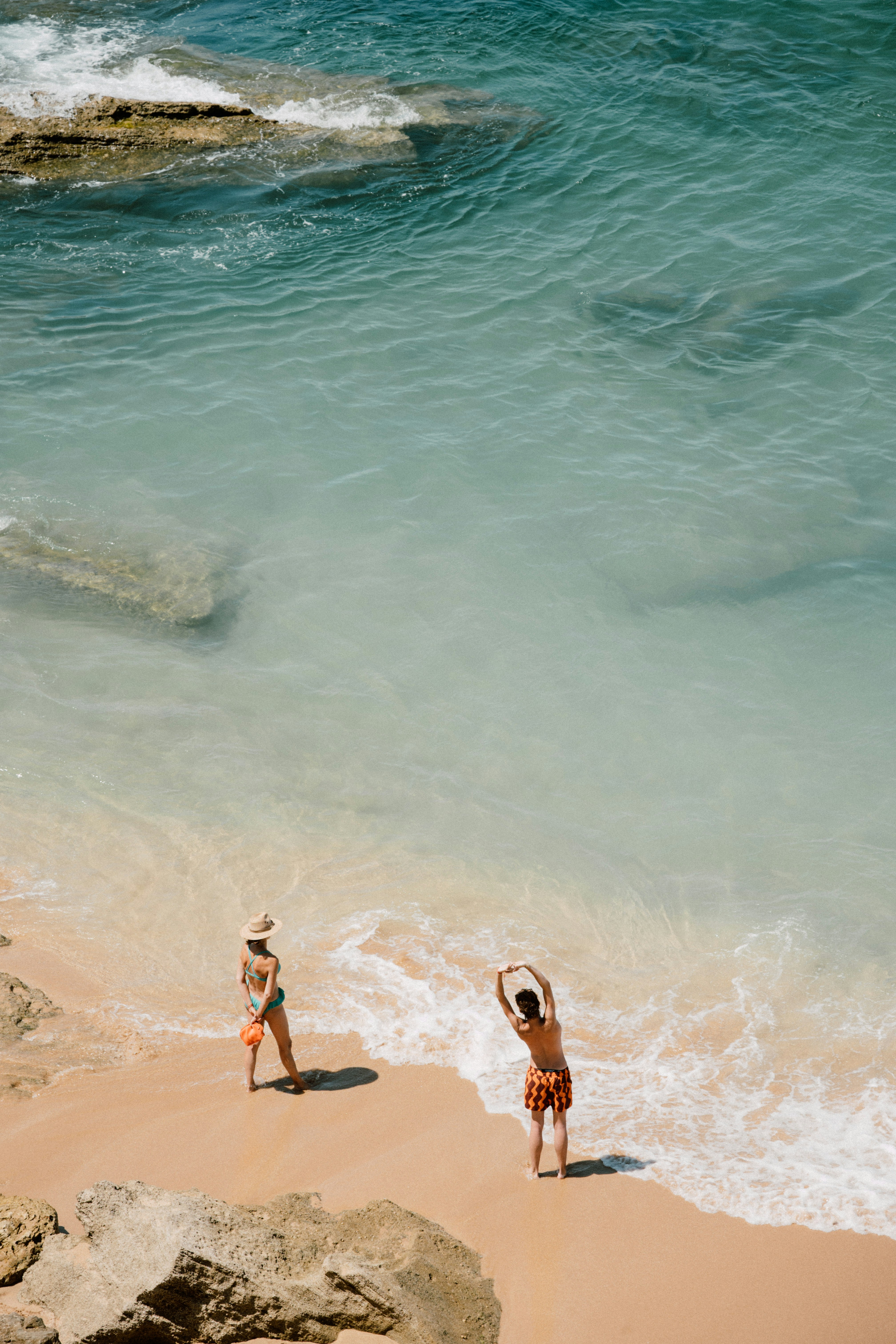 Two vacation silhouettes on sunlit shoreline under turquoise surf