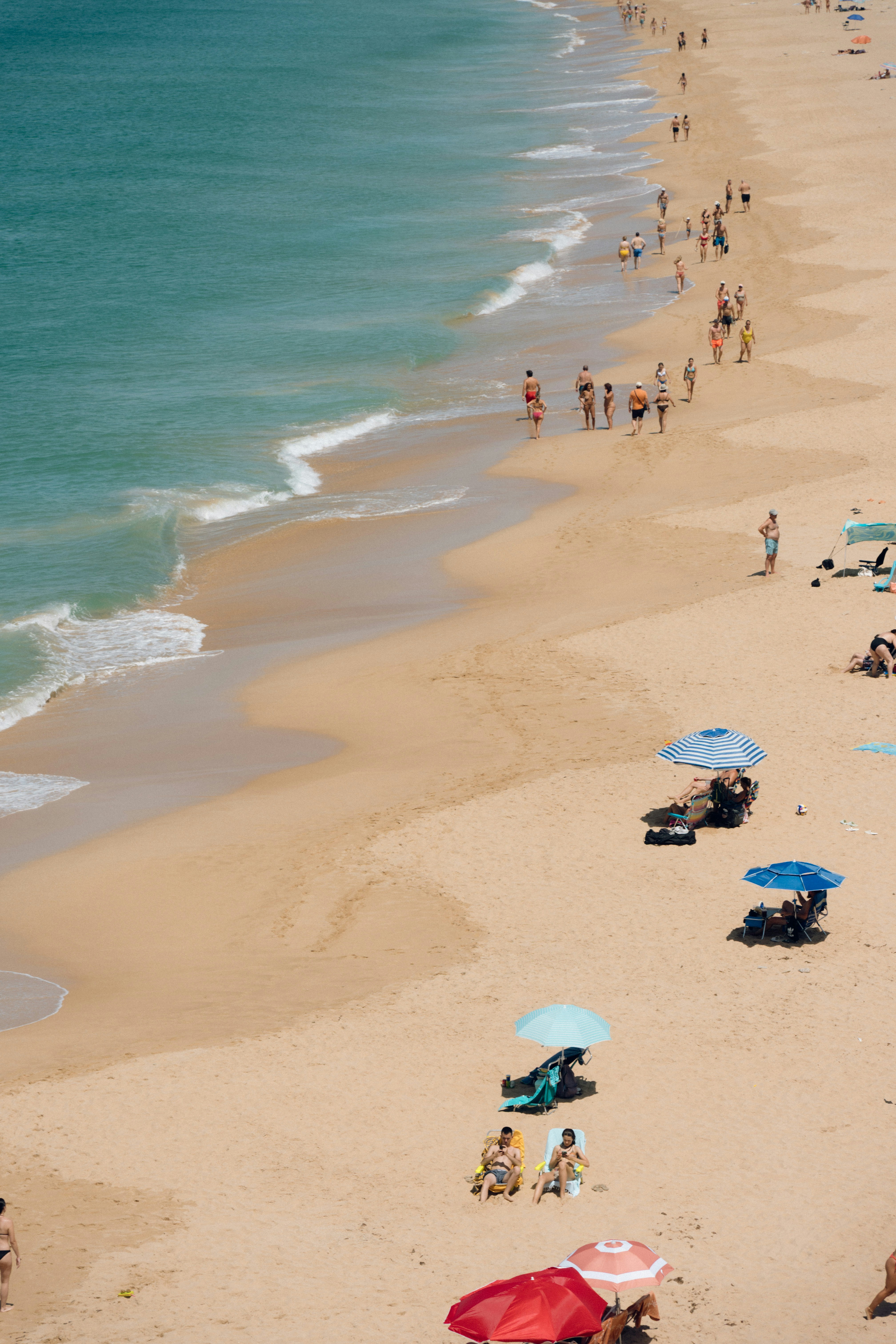 Sunlit Strand: A Recreational Line of Beachgoers Along Turquoise Waters