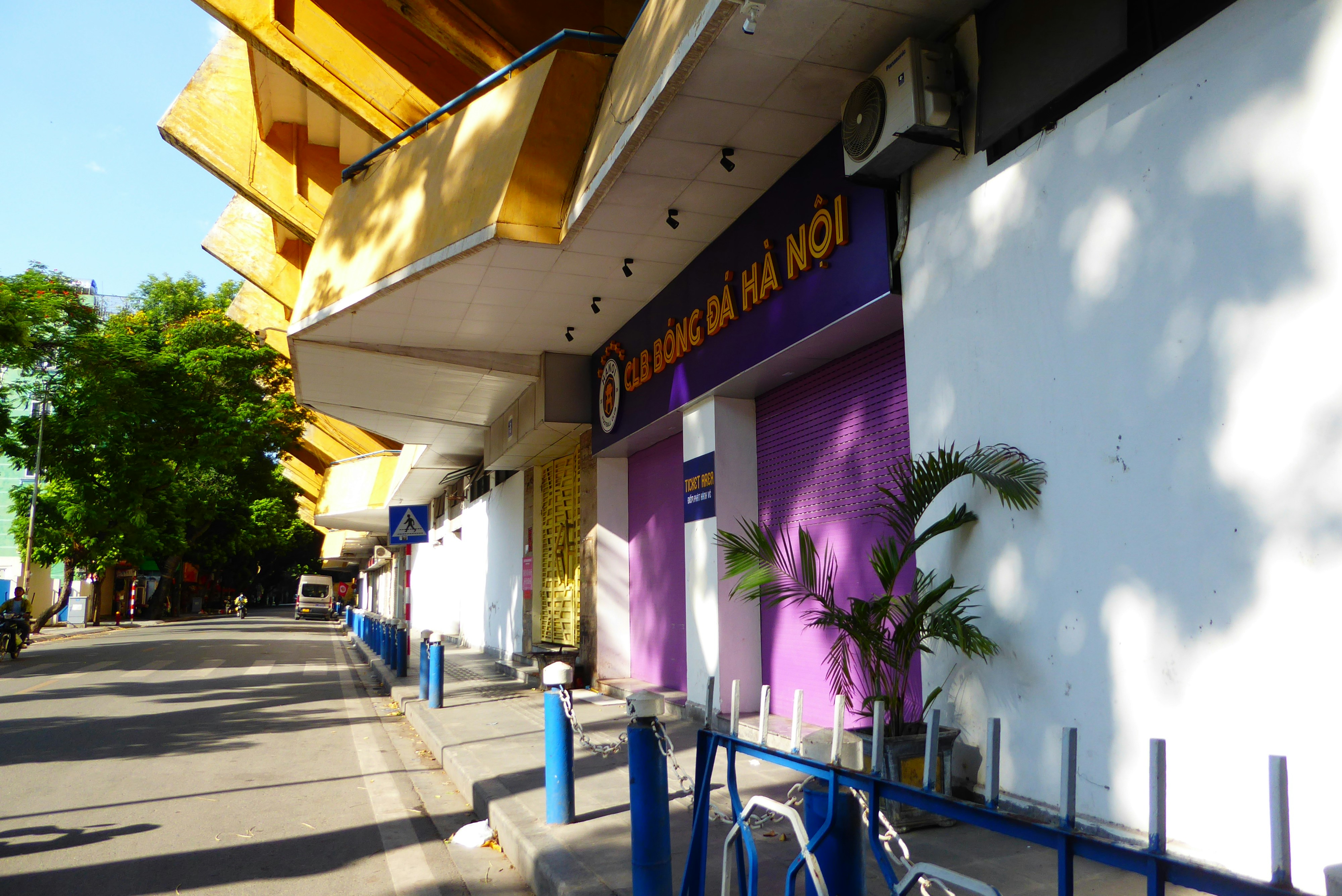 Sunlit storefronts and angular canopy cast long shadows along a quiet street