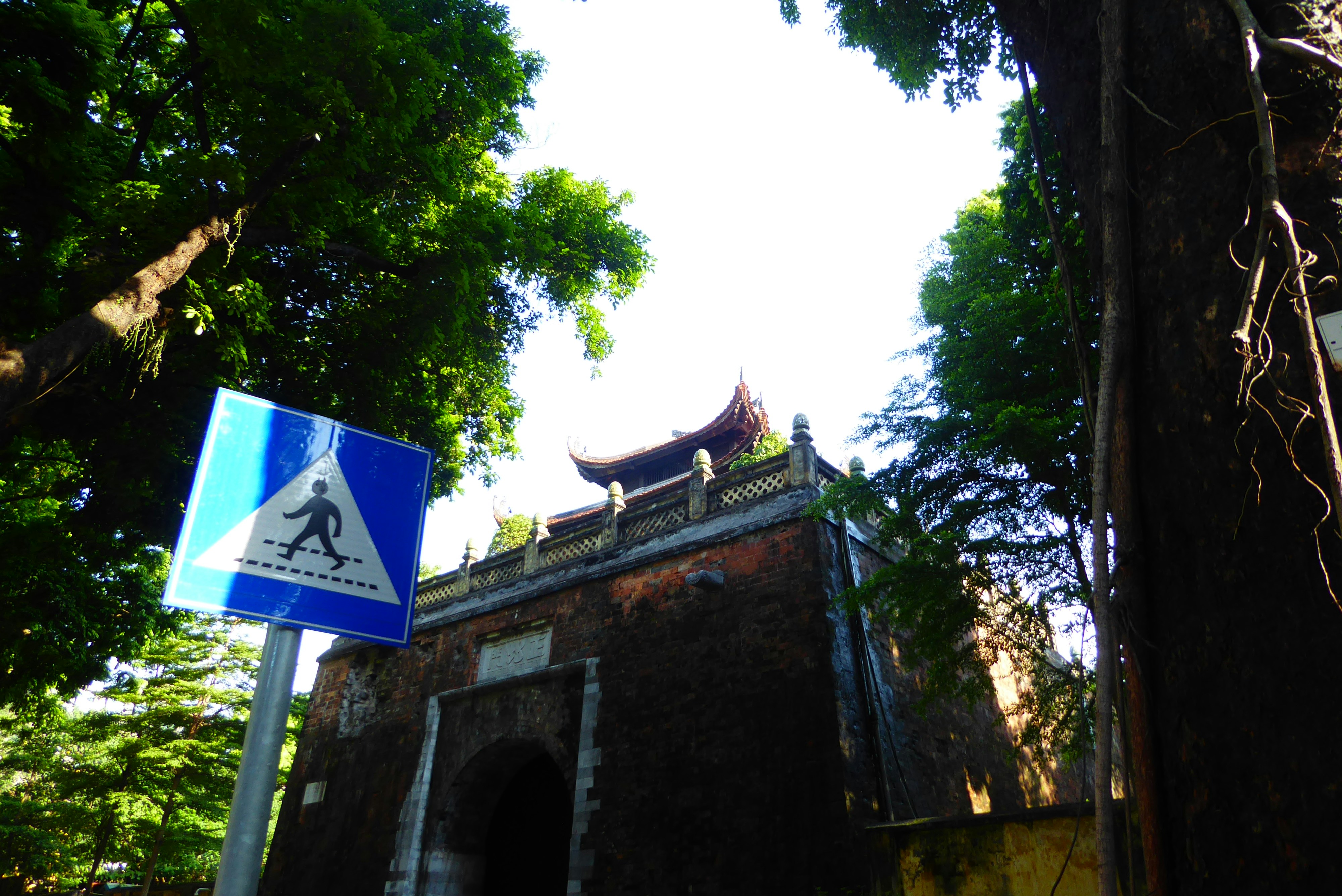 Stone gate of a historic structure framed by lush trees and a pedestrian sign in the foreground.