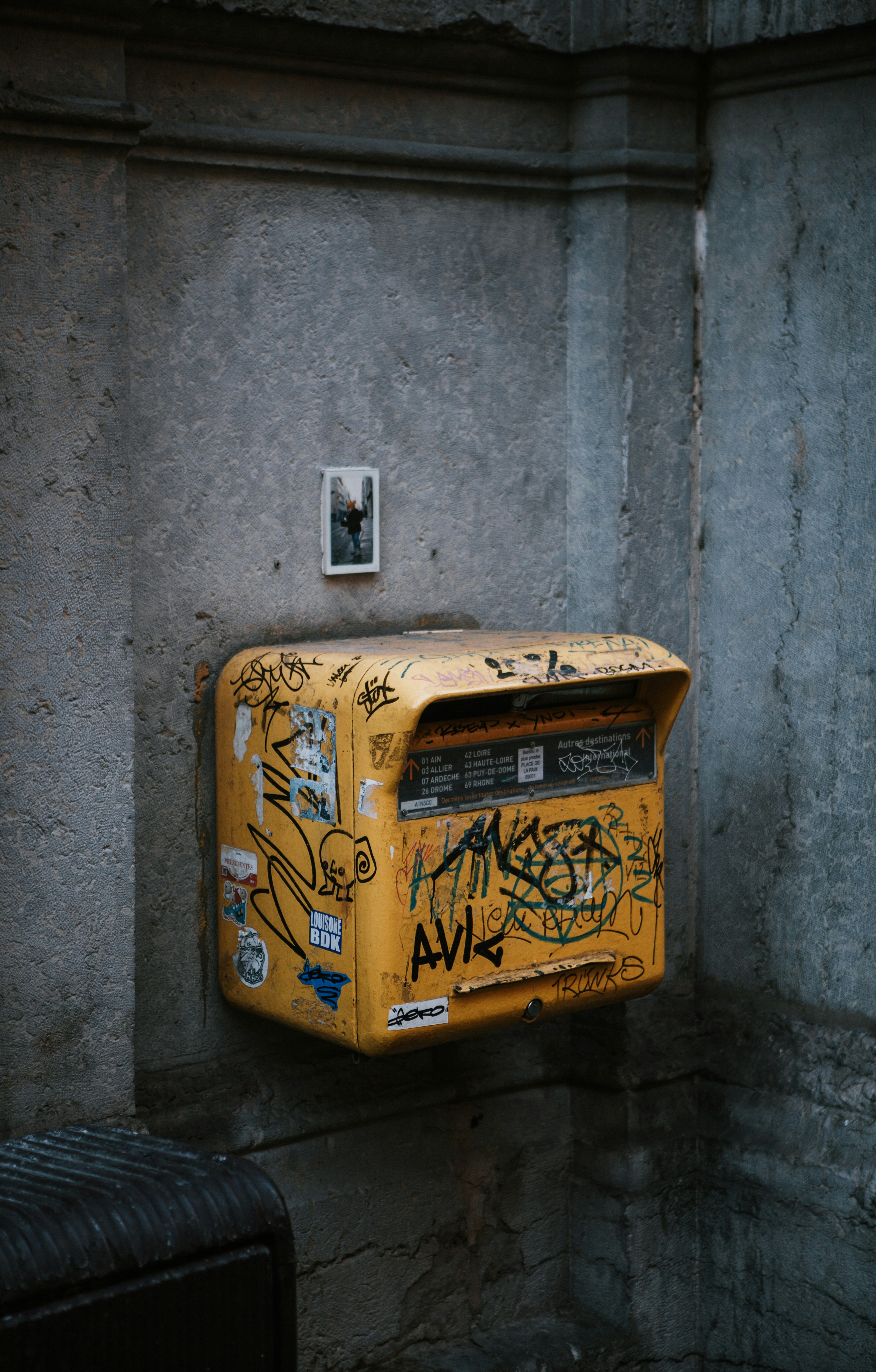 Aged yellow mailbox defaced by graffiti beneath stone arches
