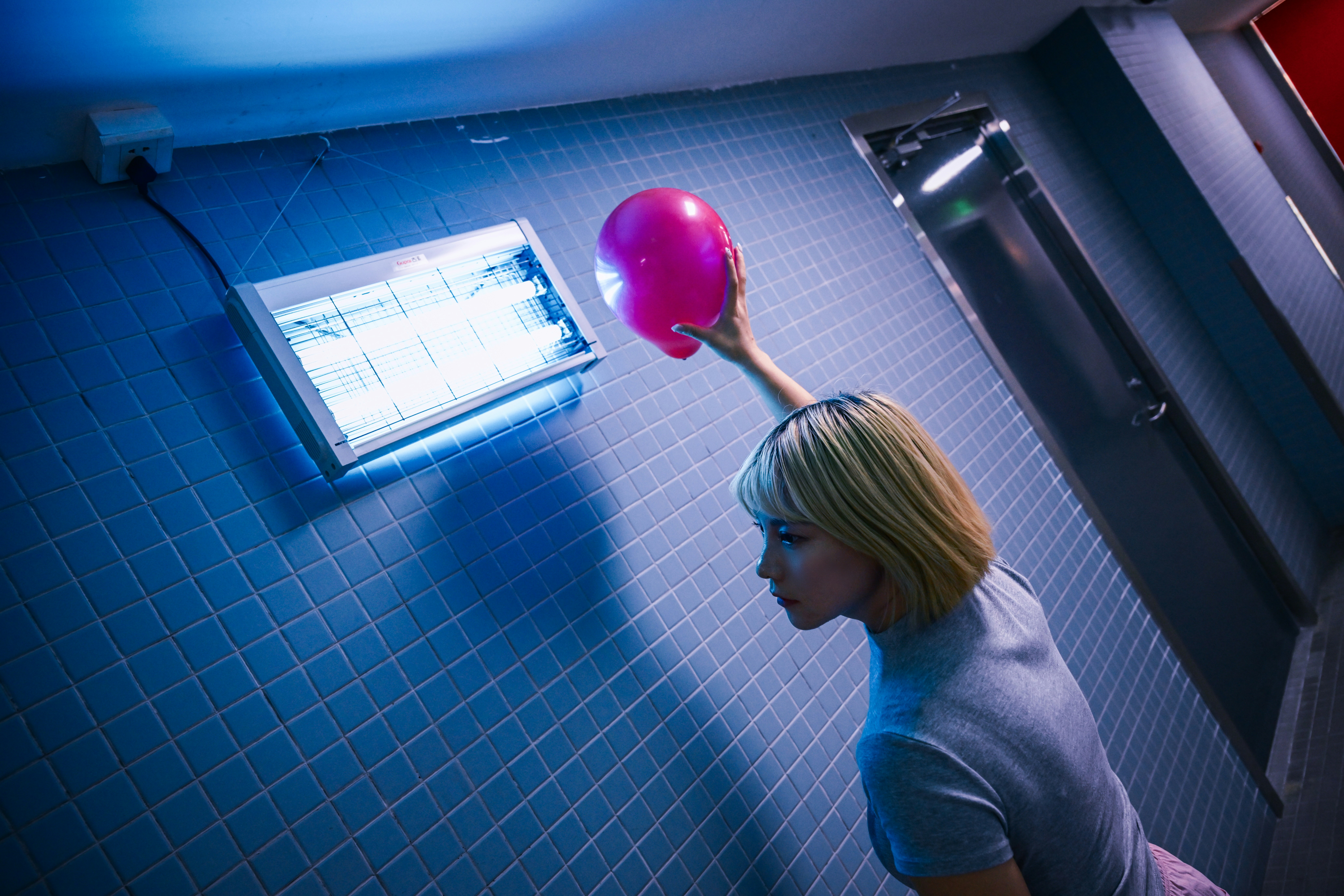 Holding the Moment: A Pink Balloon in a Neon-Blue Corridor