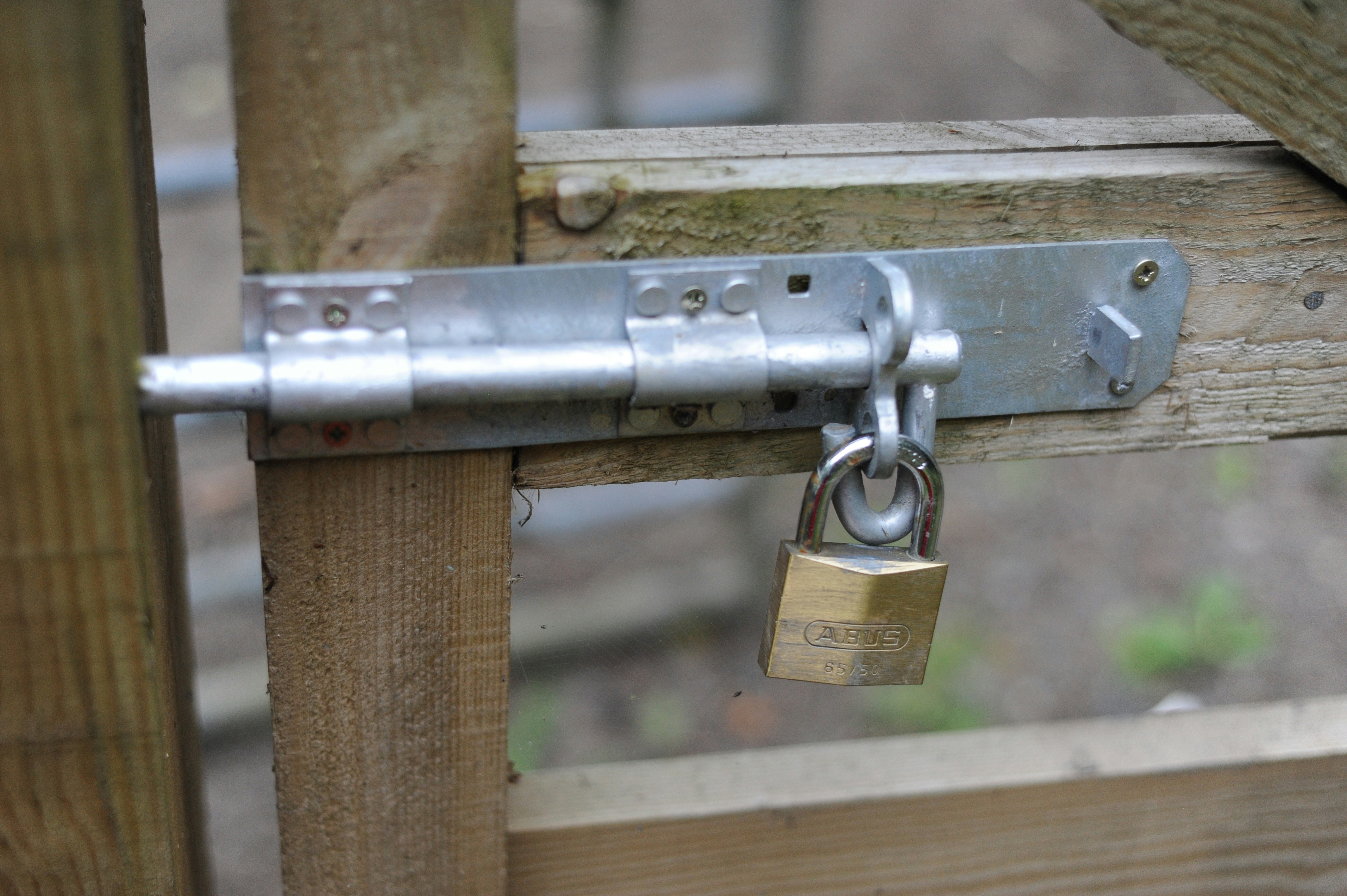 Padlock on a weathered latch securing a rustic wooden gate