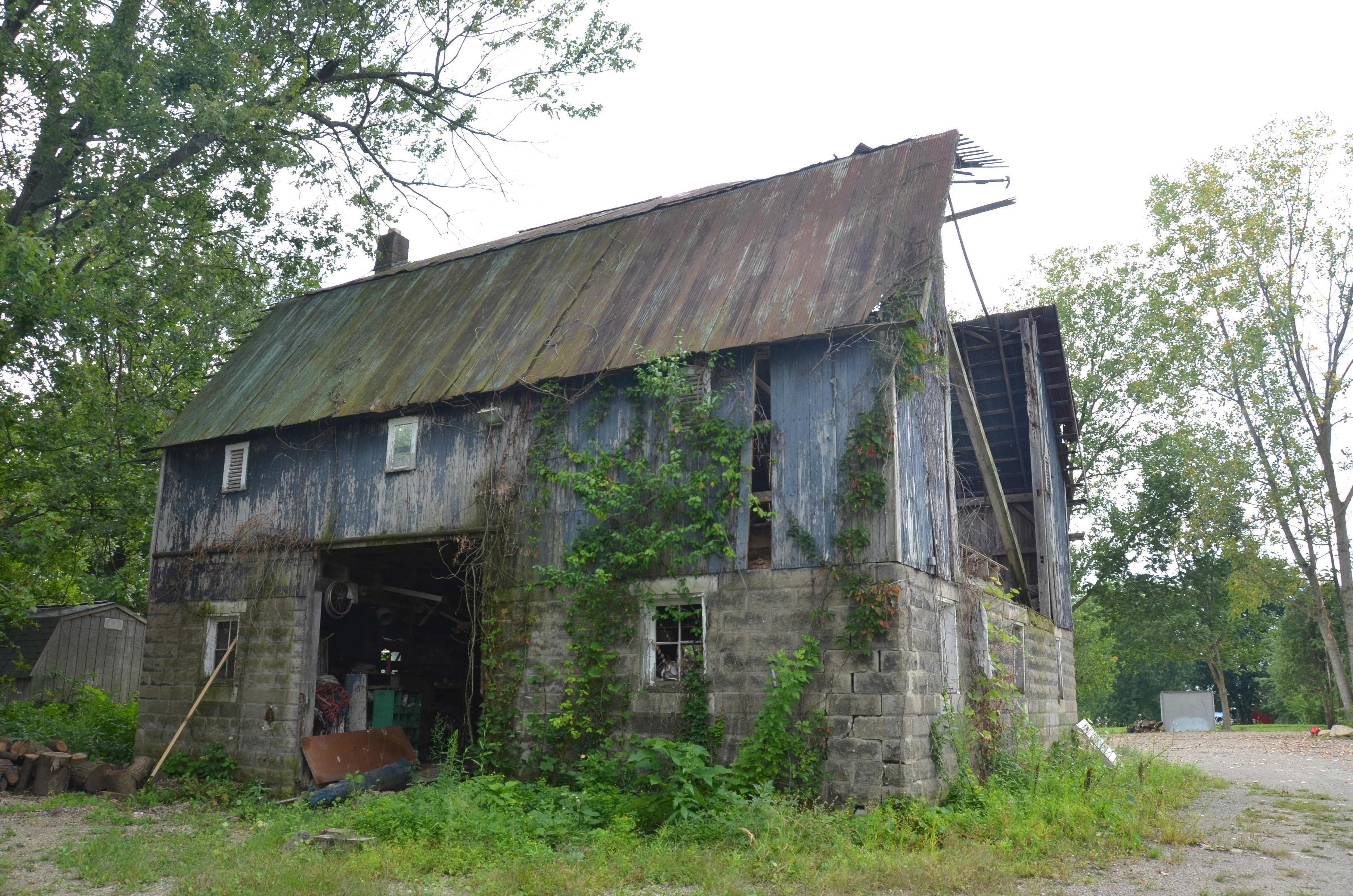 Weathered barn with ivy-clad stone base against a green backdrop