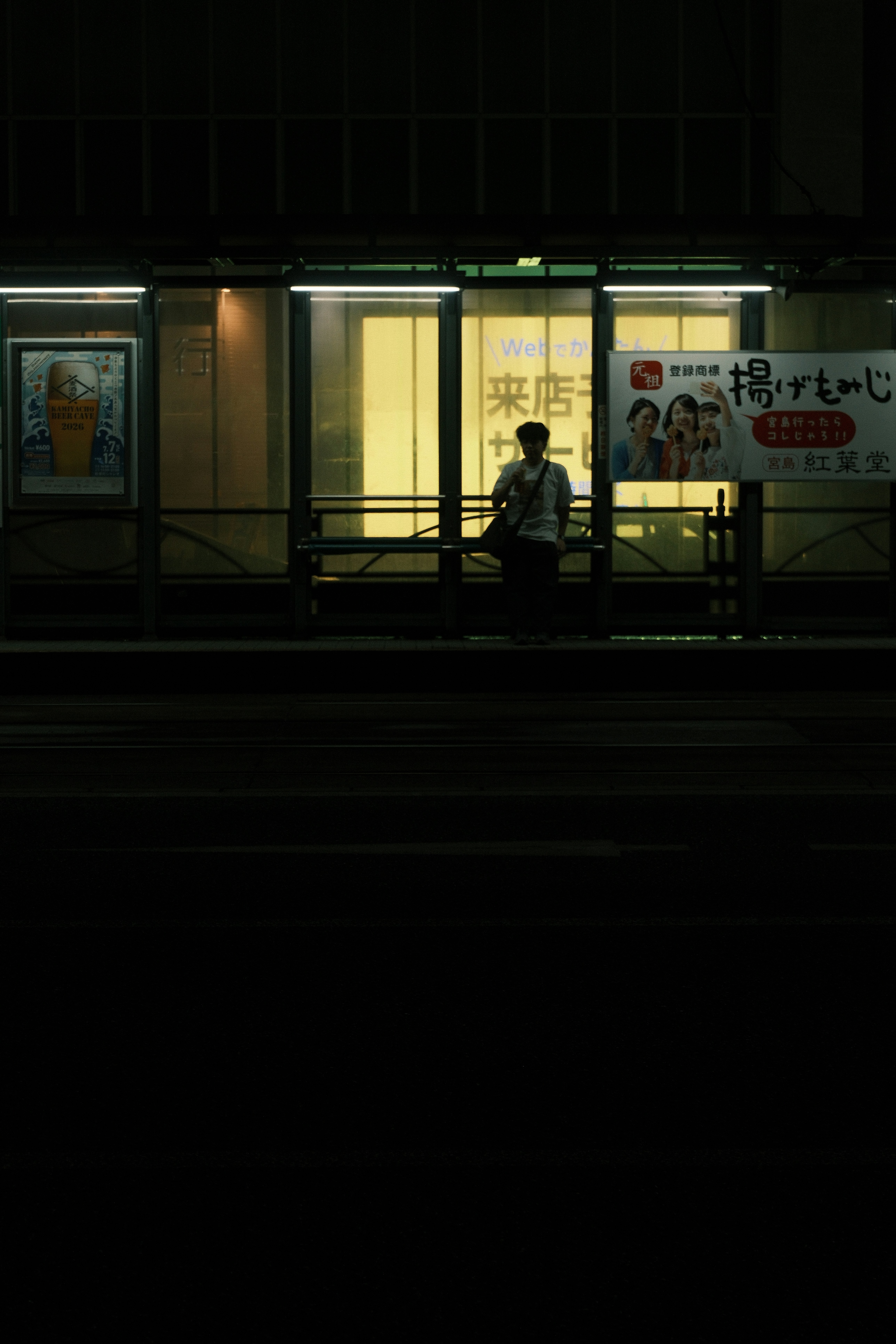 A person waiting at a brightly lit tram stop at night in Japan