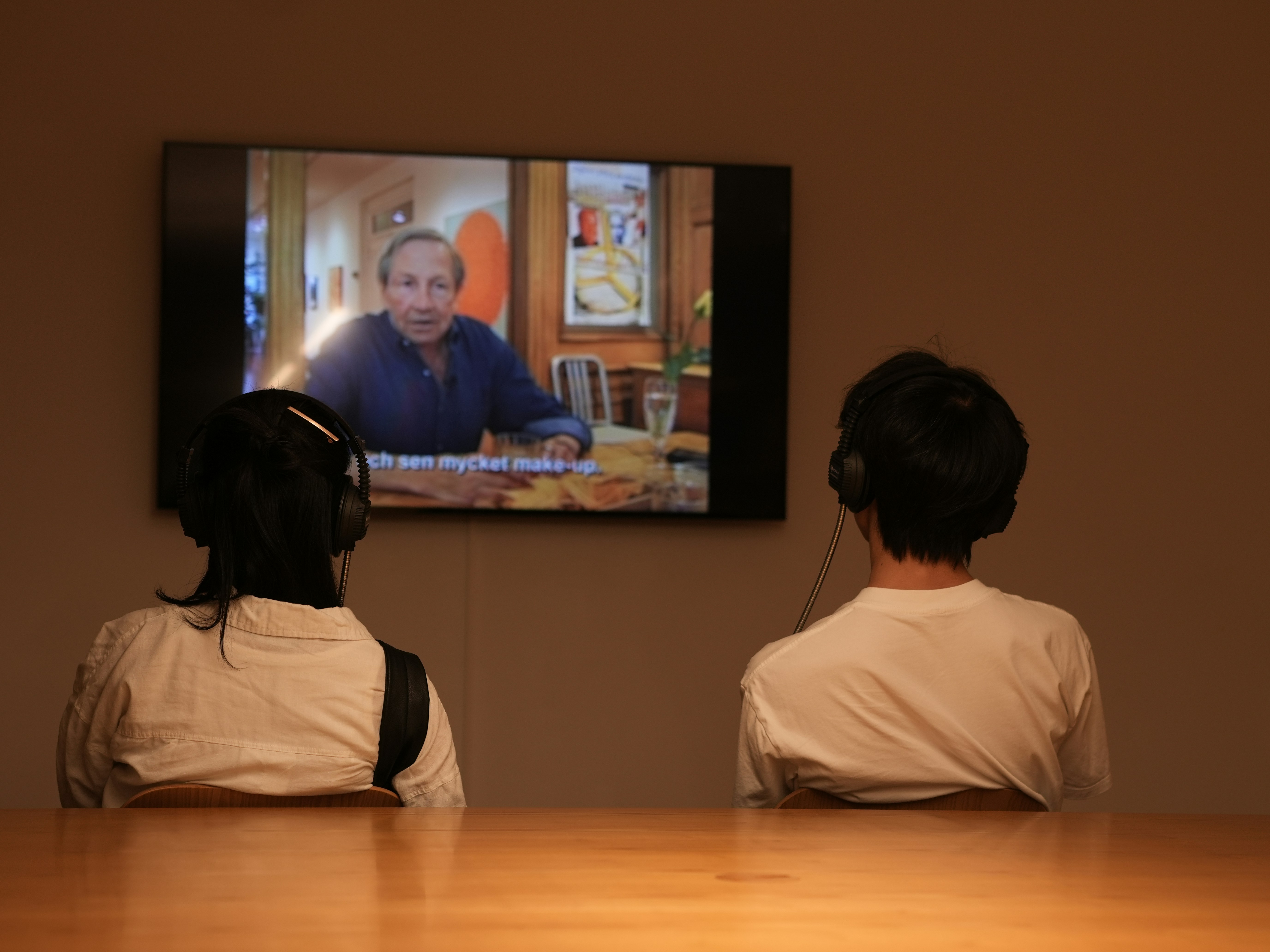 Silent Cinema: Two viewers fixate on a warm interview on the wall-mounted screen