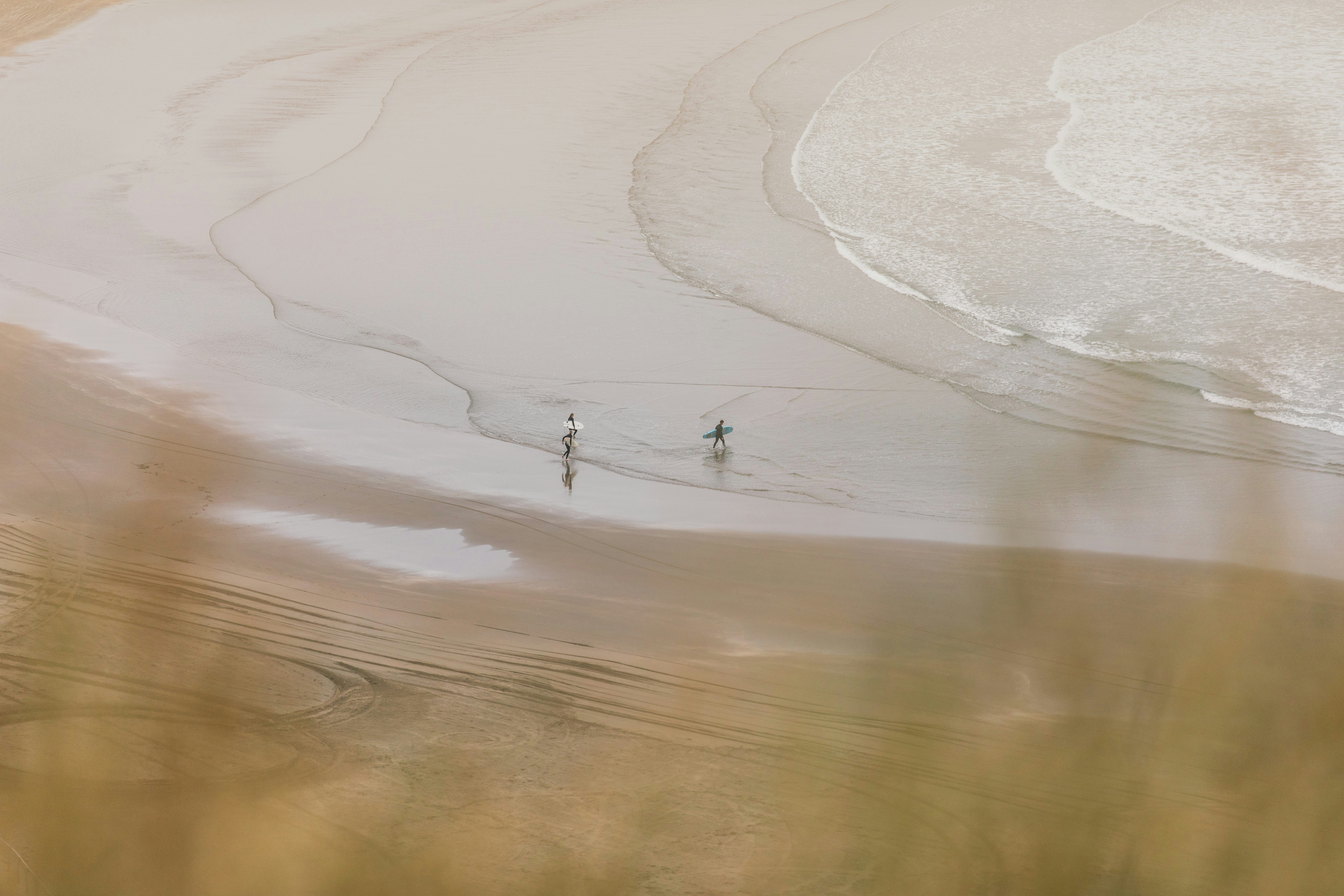 Two surfers on a misty shoreline as waves cradle the shore
