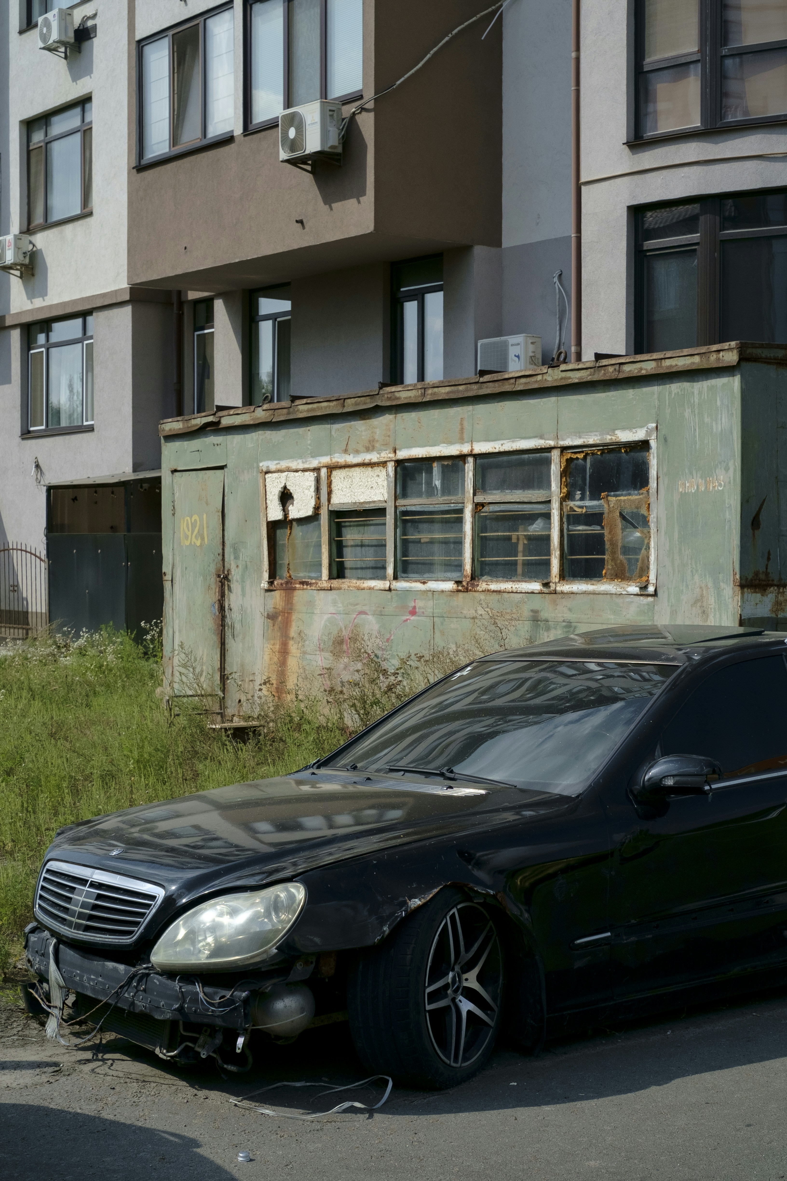 Rust and Reflections: A Dilapidated Keep Stall Behind a Not-So-Sleek Sedan