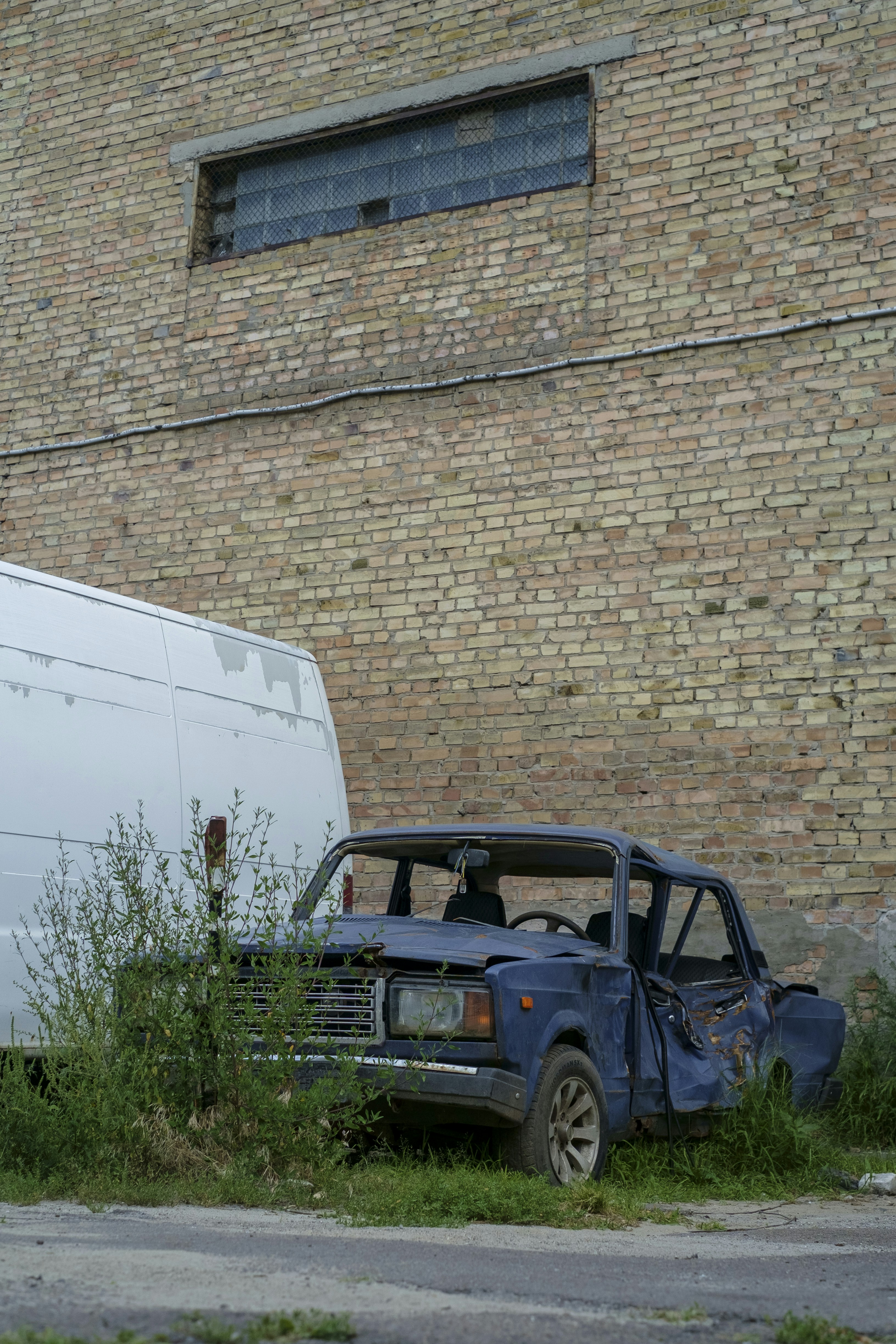 Abandoned blue car at the edge of a brick wall