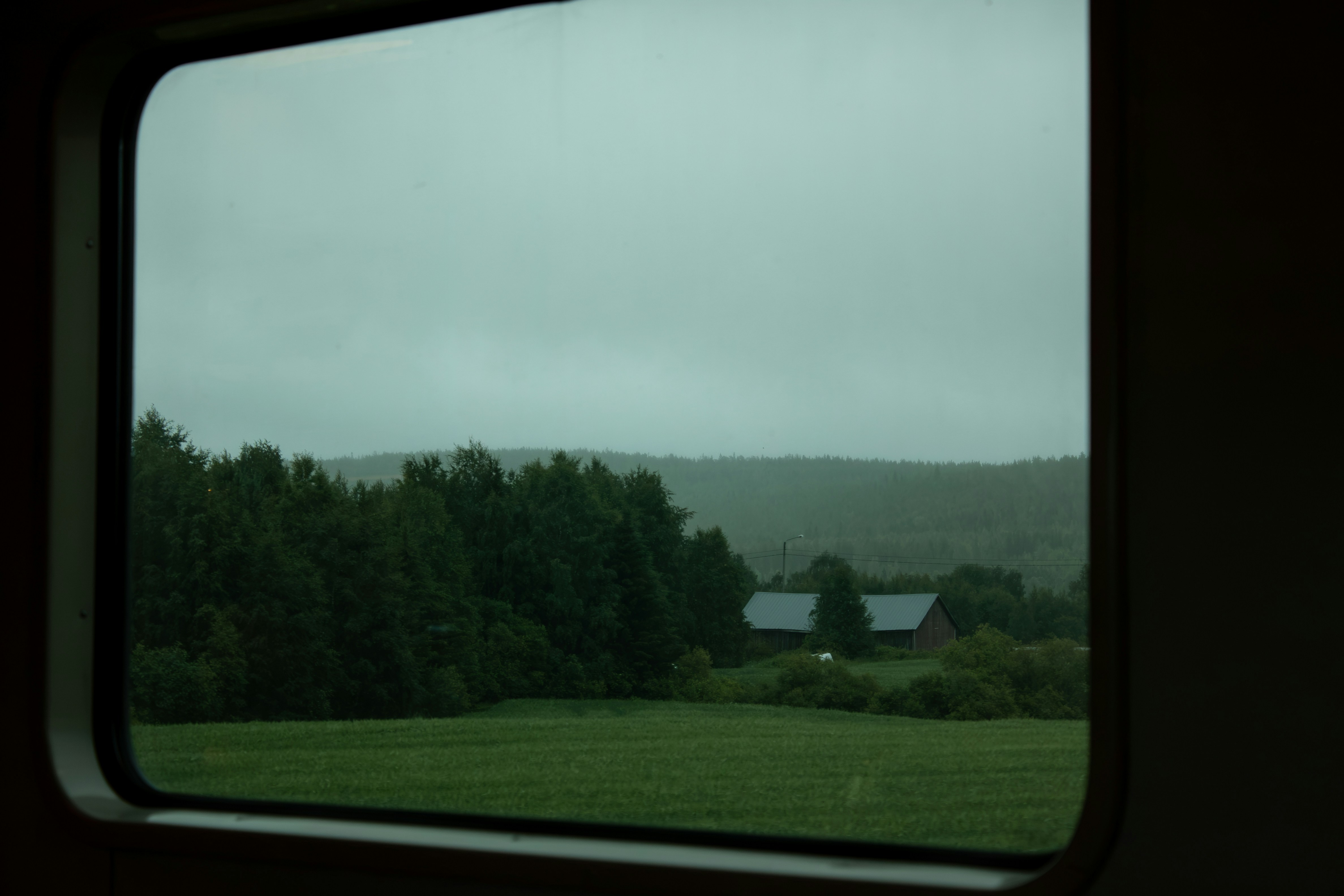 Muted rural landscape visible through a rectangular window, featuring a distant barn and treeline under overcast skies.