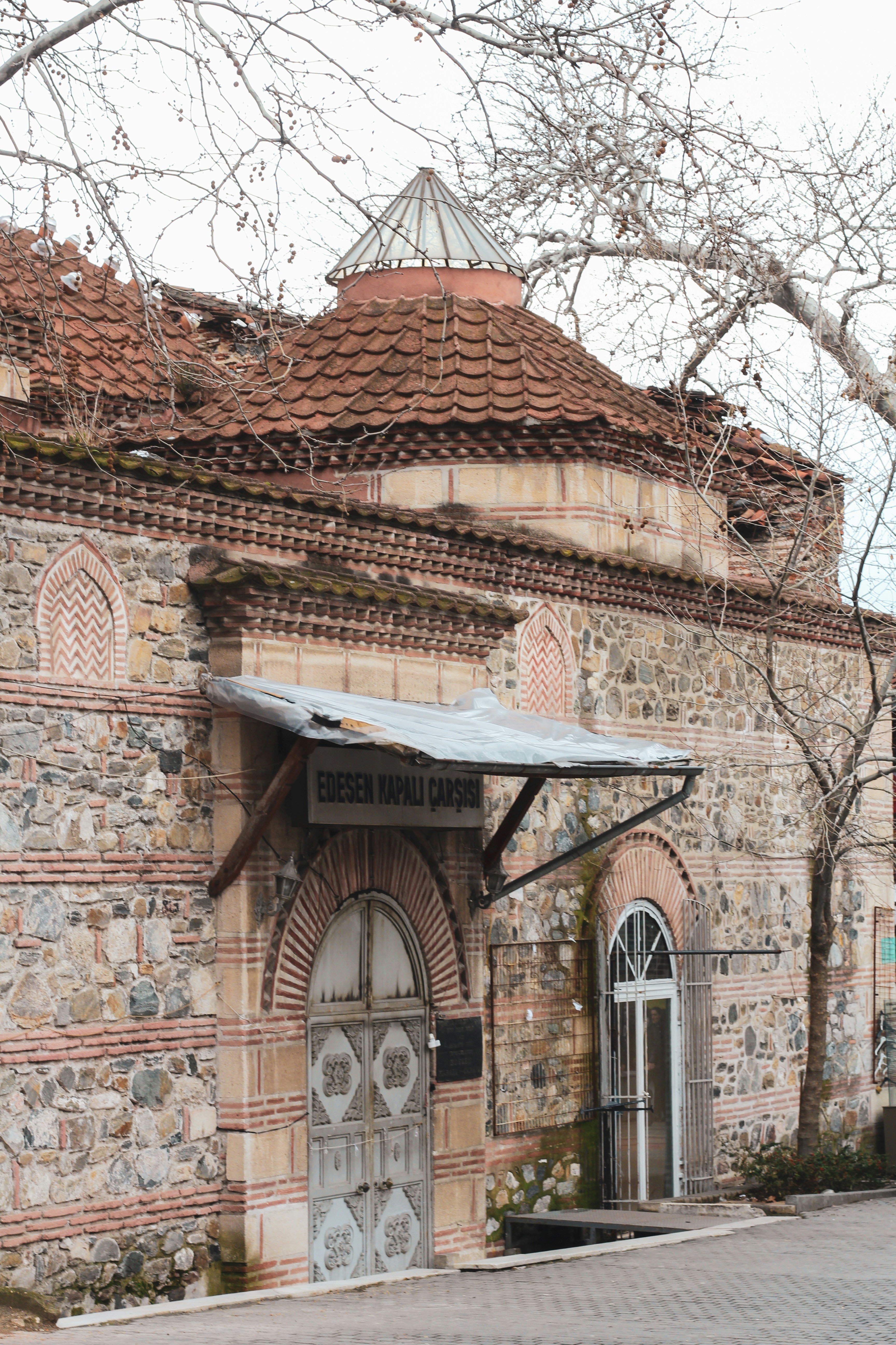 Rustic stone chapel with arched entry and tiled roof under bare winter branches
