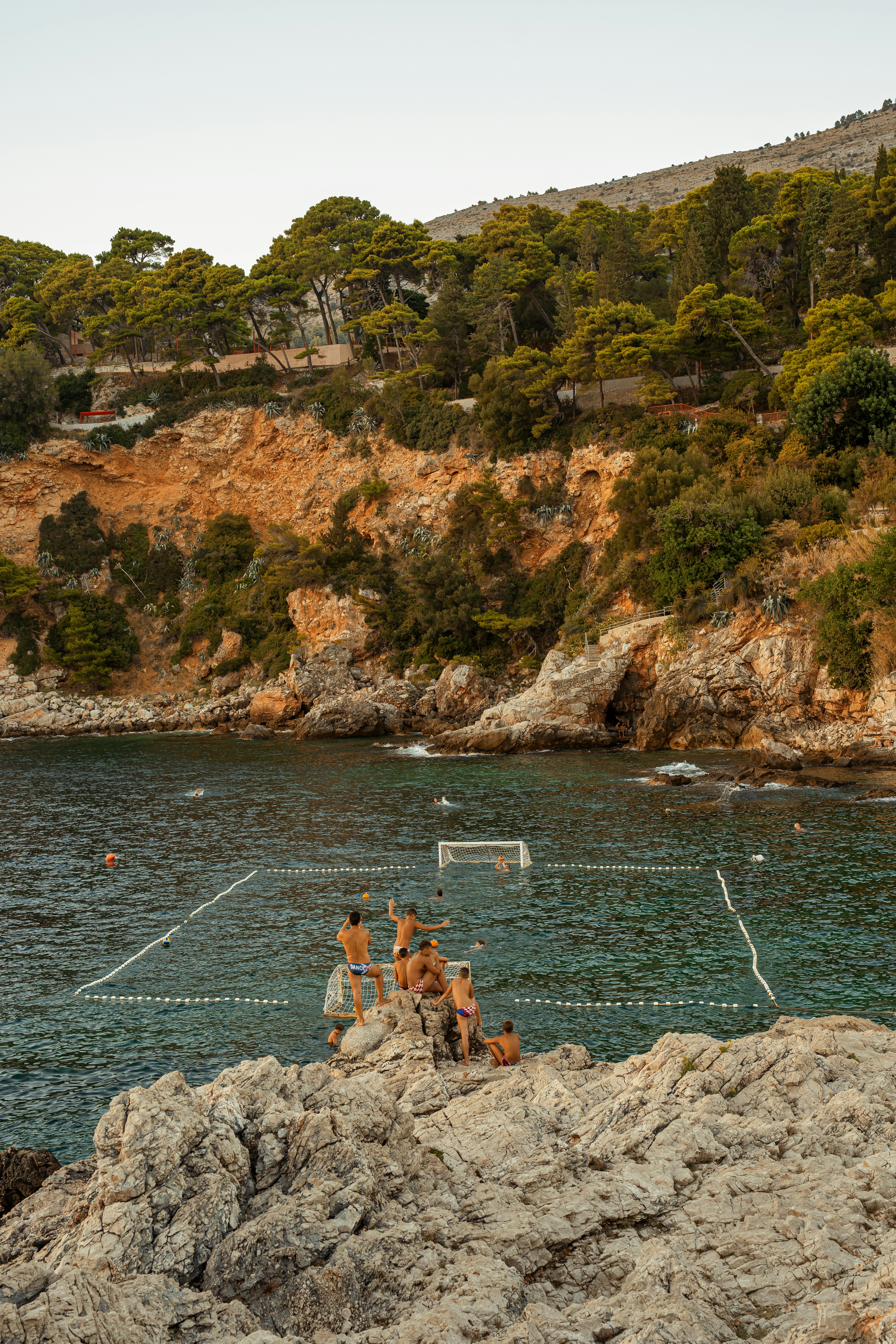 Rugged shoreline courtyard: swimmers in a tethered net anchored to rocky outcrop