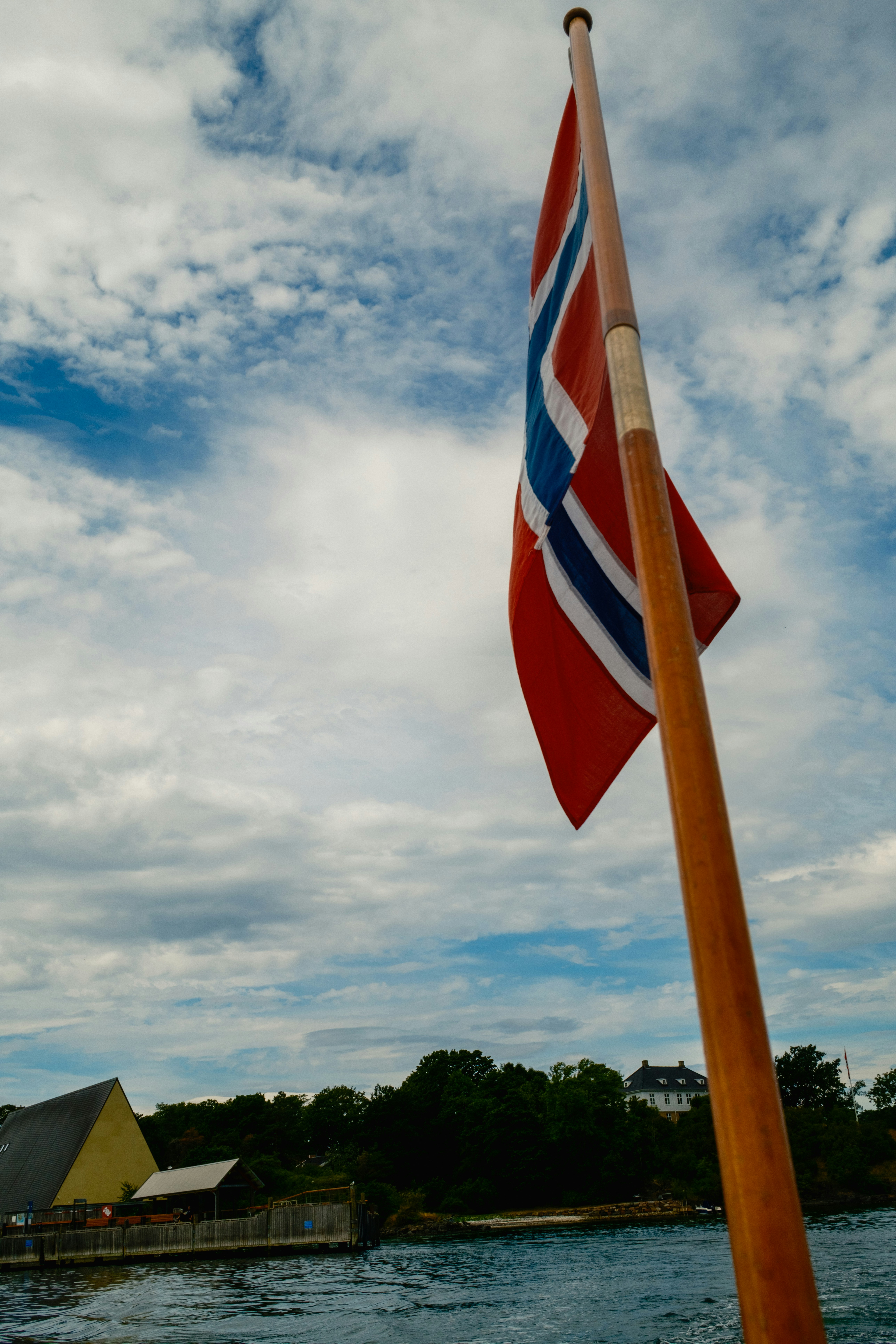 Norwegian Flag on a Tall Mast Against a Cloudy Sky