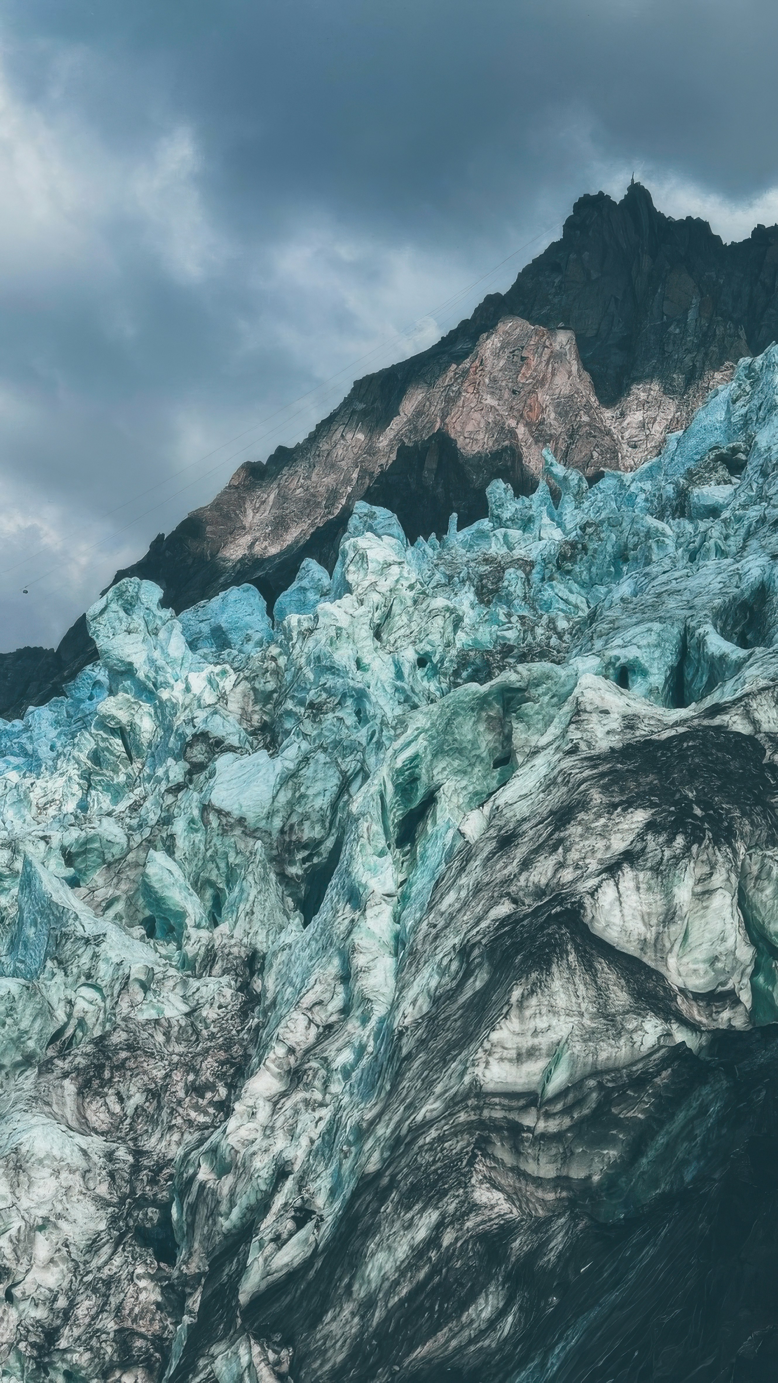 Jagged glacier tongue and rocky peak under moody clouds, with blue-tinged ice dominating the lower slope.