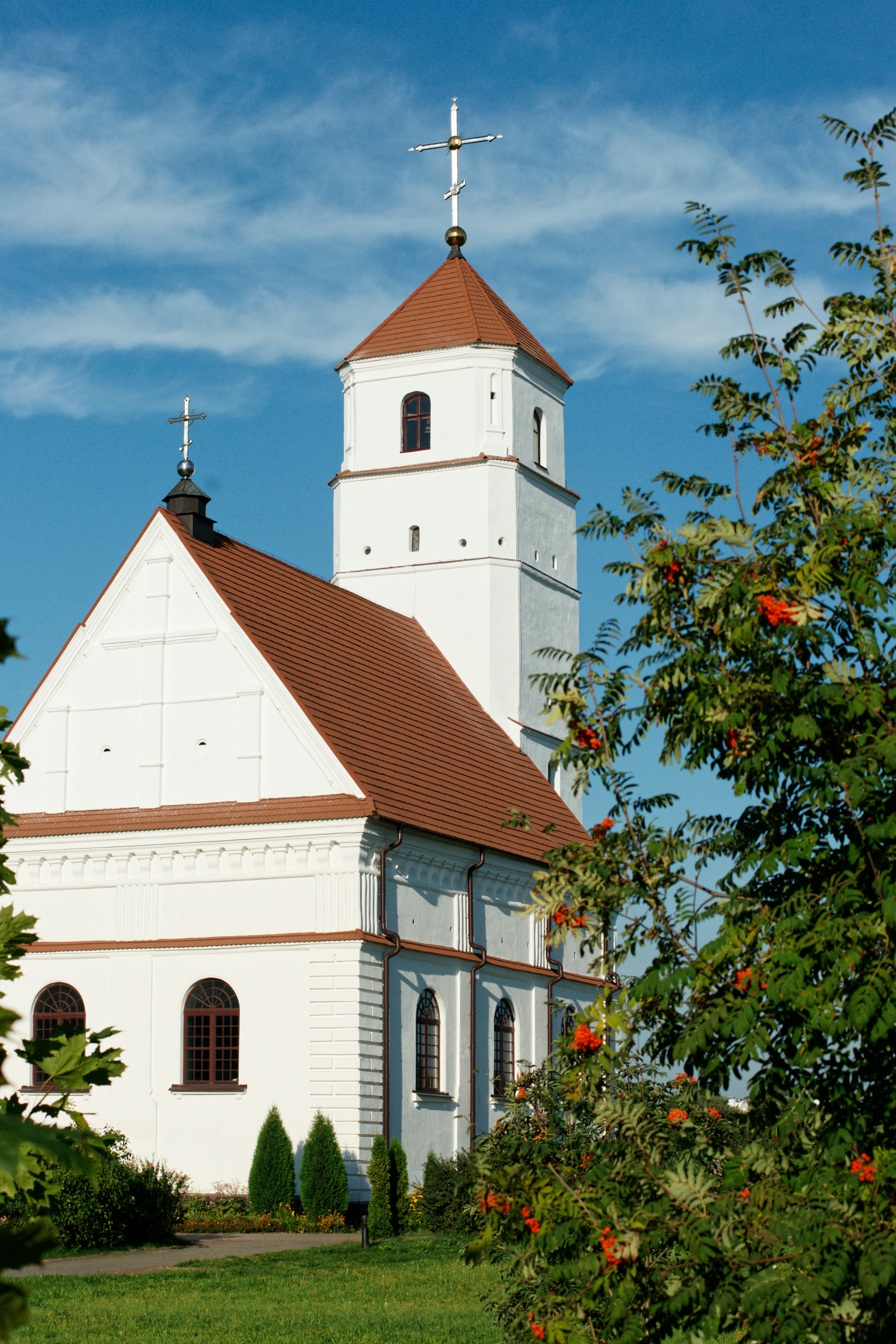 A white church with a tall steeple sits amid greenery under a blue sky; the composition emphasizes architecture and surrounding trees.