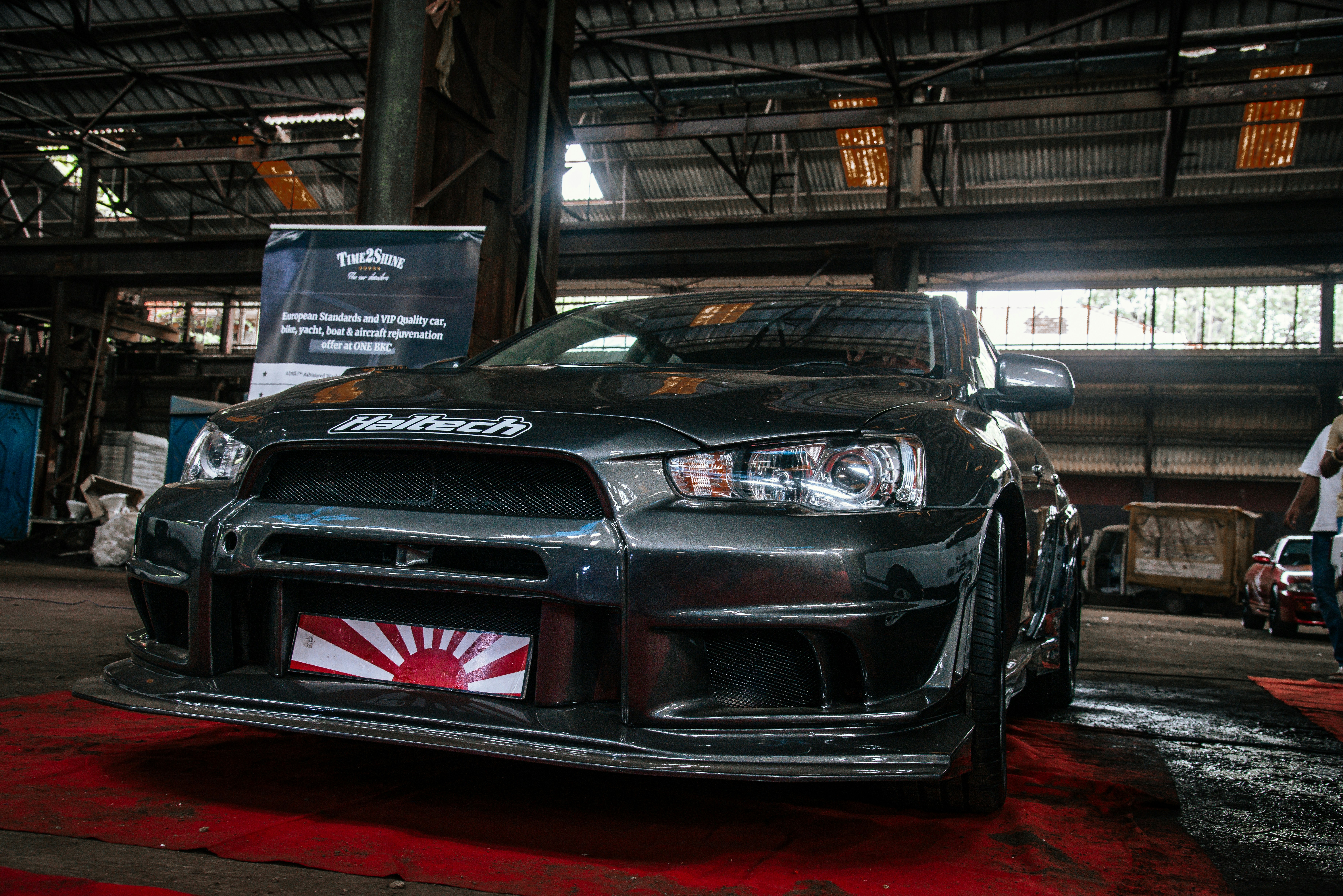 Low-angle stance: a tuned rally street sedan on a red carpet in a dim industrial hall