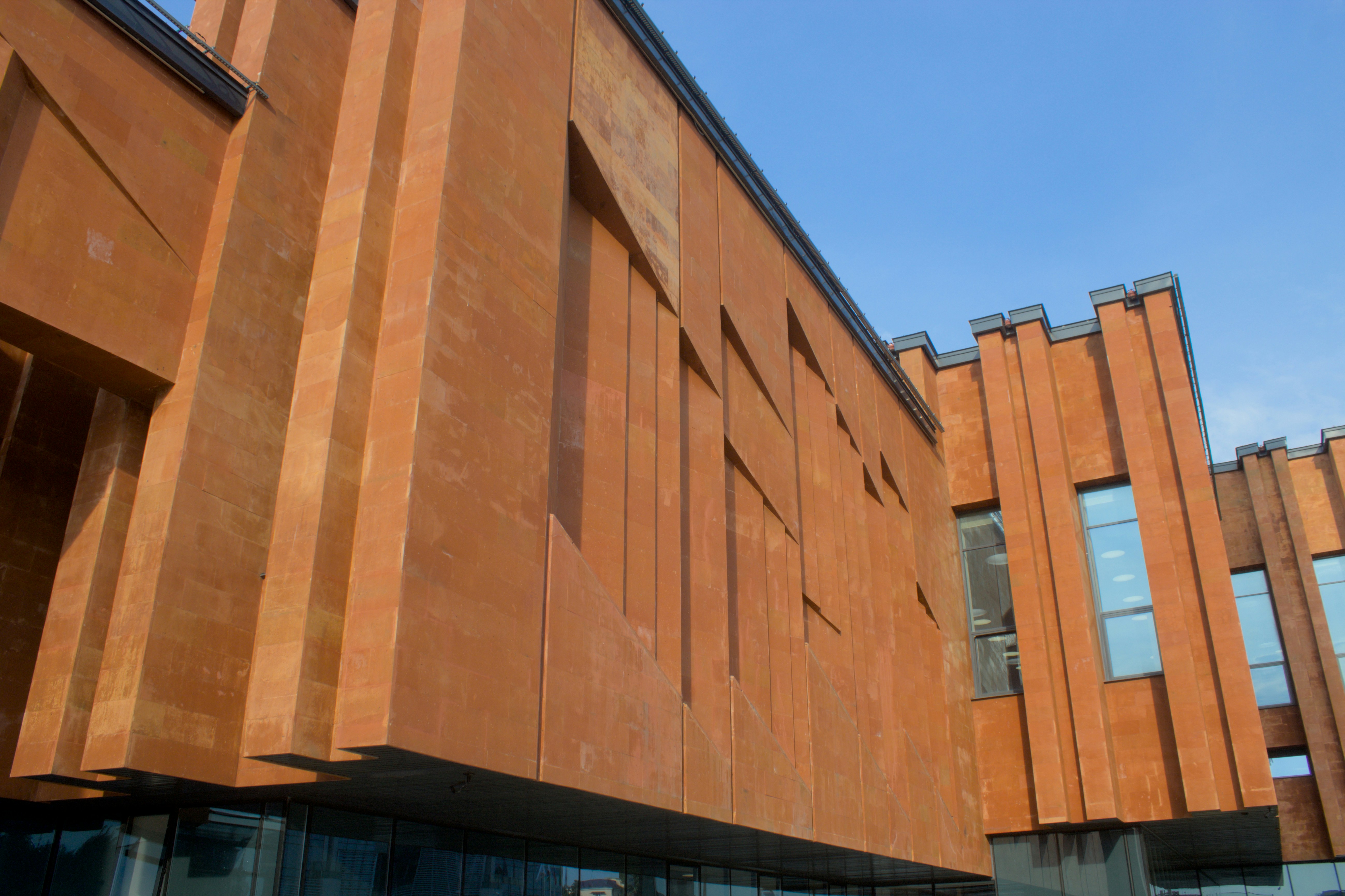 Rust-red Geometry: A Modern Brick Facade Rising Against a Clear Sky