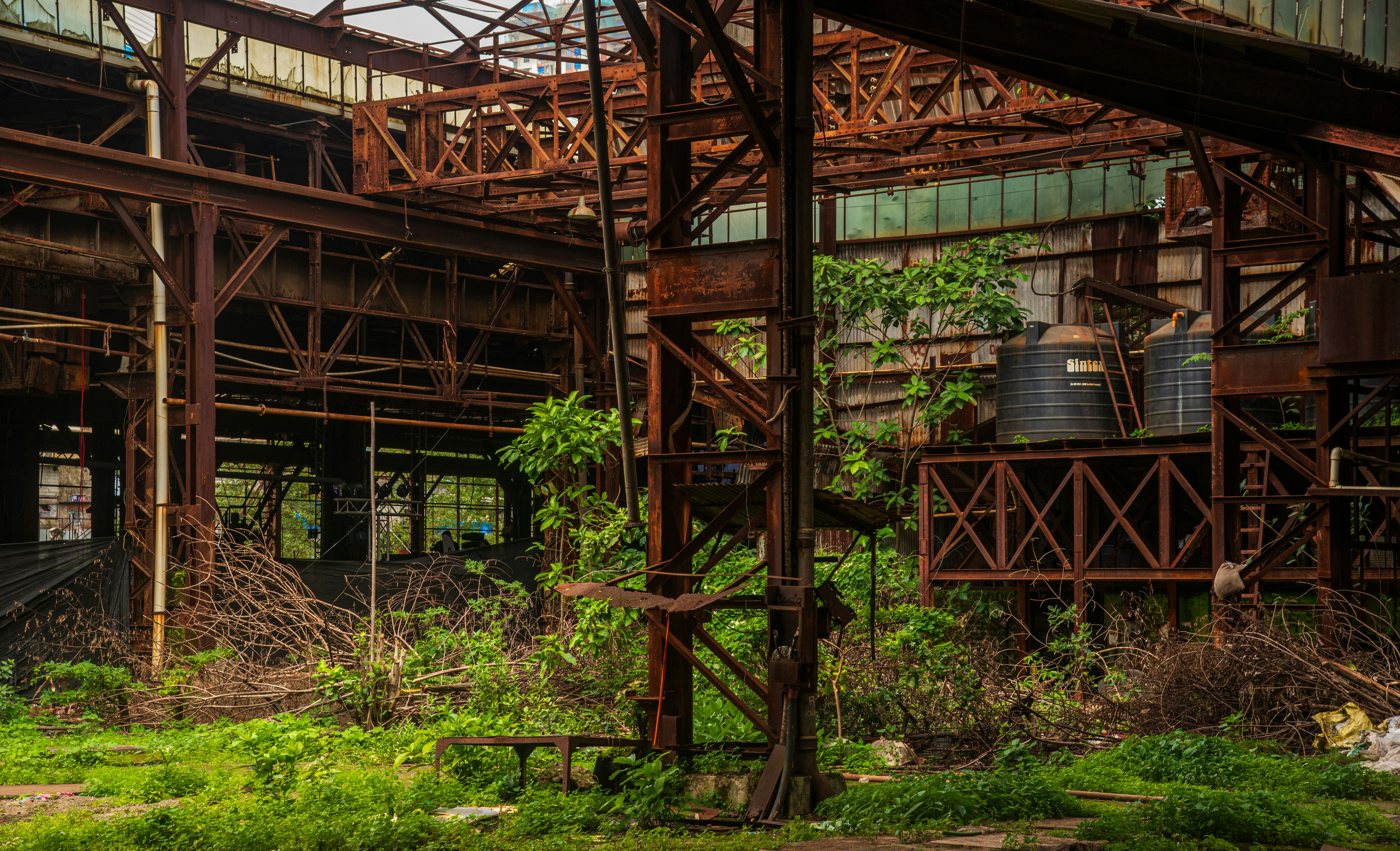 Industrial ruins overrun by greenery, with weathered steel beams and scattered vegetation forming a cityscape of decay.