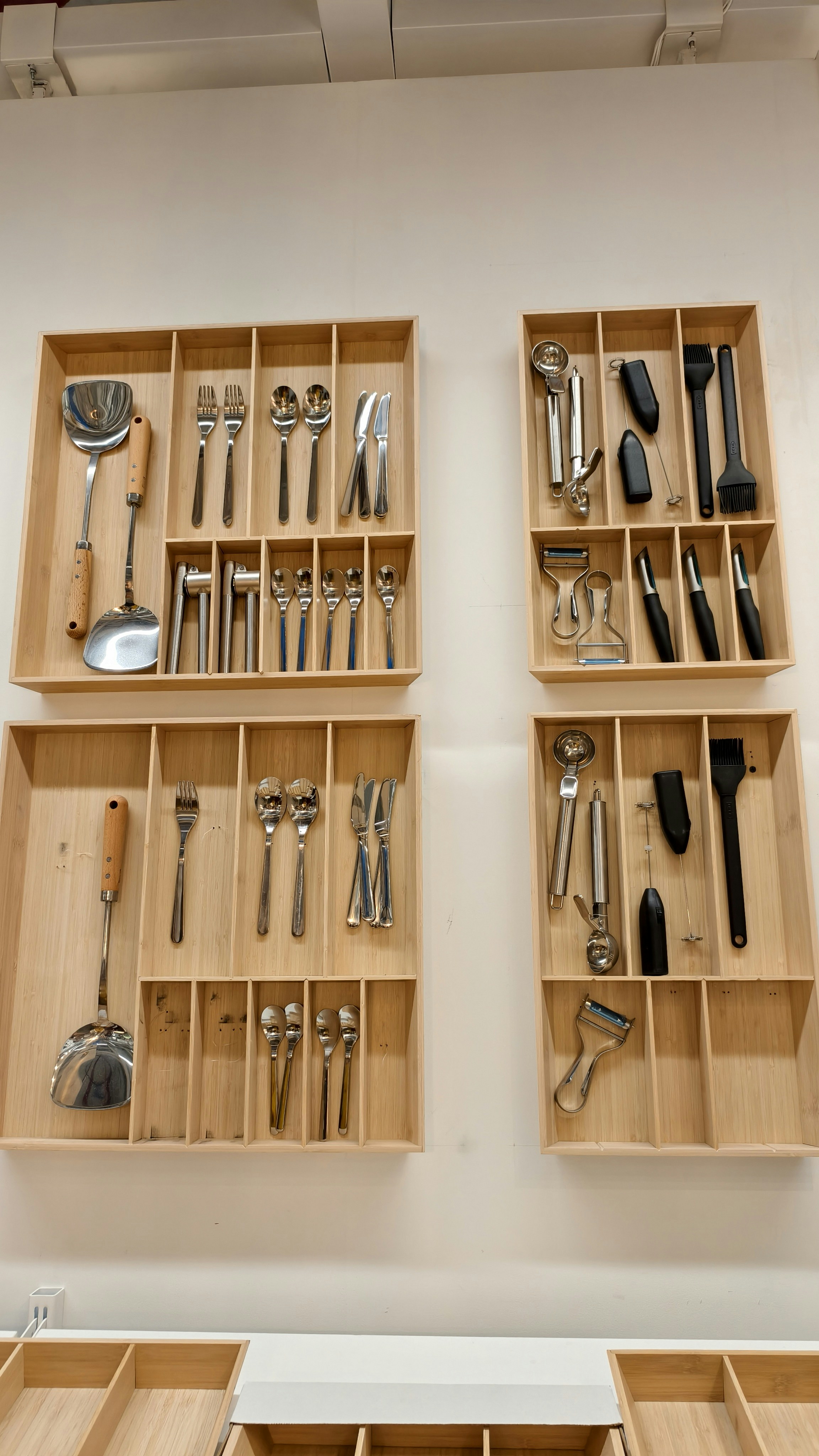 Assorted forks, spoons, and kitchen tools arranged in wooden compartments on a wall display.