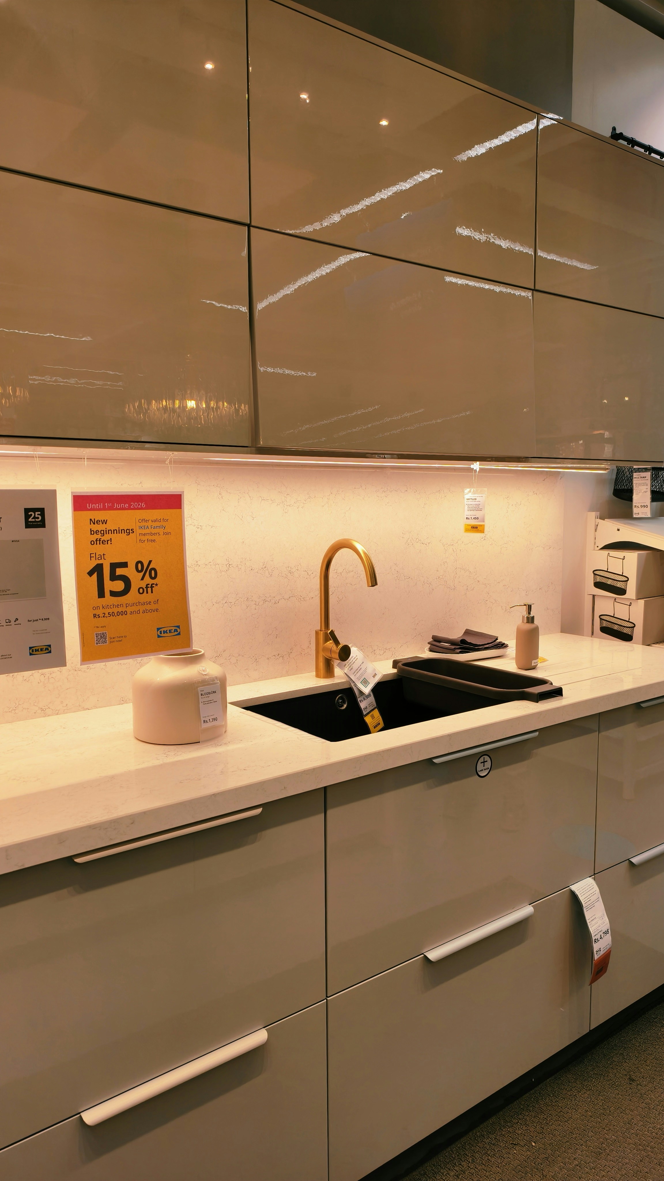 Creamy kitchen showroom with a gold curved faucet, sink, and marble countertop.