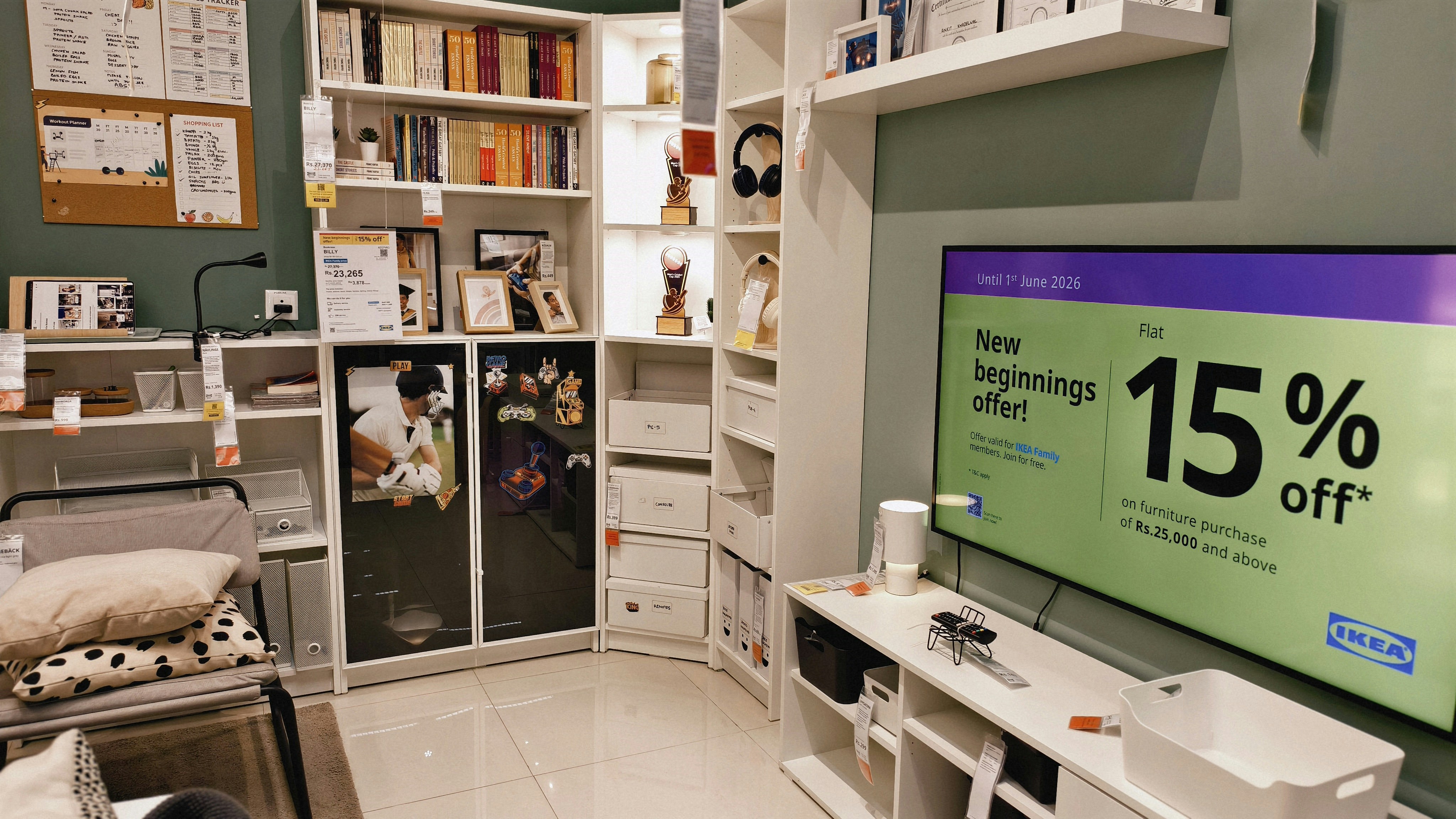 A tidy showroom scene with a large wall-mounted TV displaying a bold 15% off graphic, surrounded by shelving and a neatly arranged seating area. The setting resembles a product display or showroom space rather than a candid home interior.